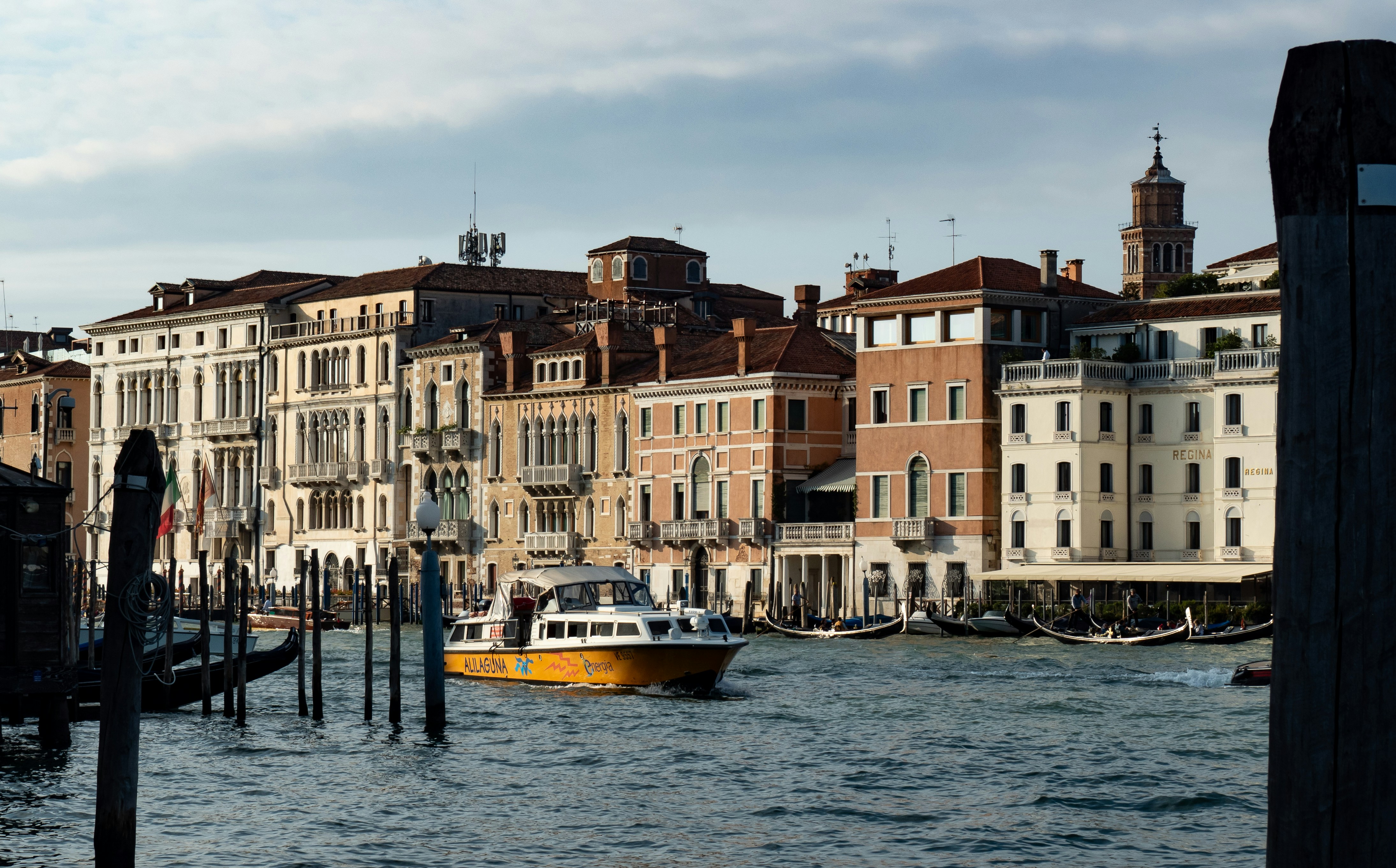 Yellow boat navigating the canal with historic Venetian buildings under a partly cloudy sky.