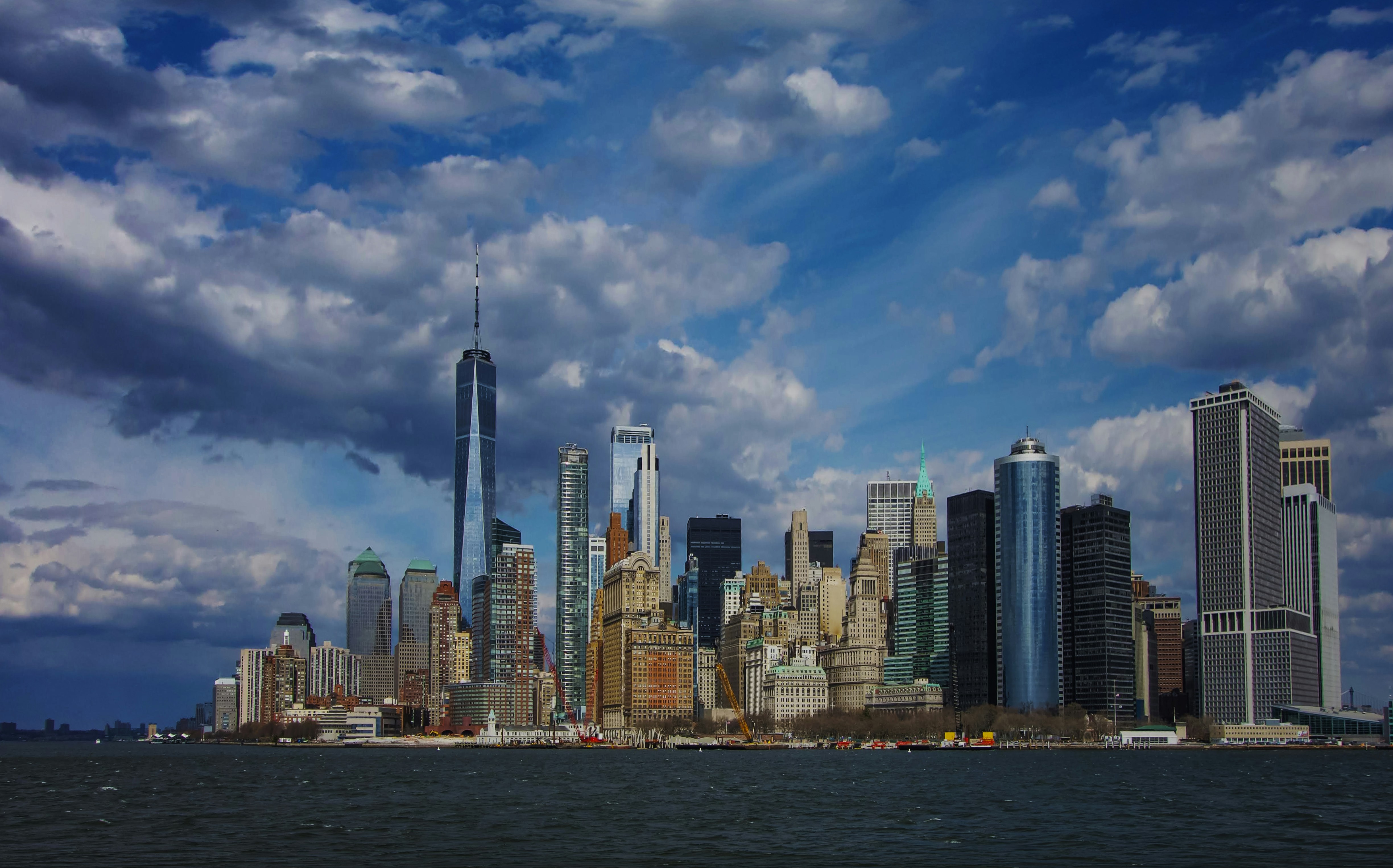 Dramatic clouds cast shadows over a city skyline with towering buildings.