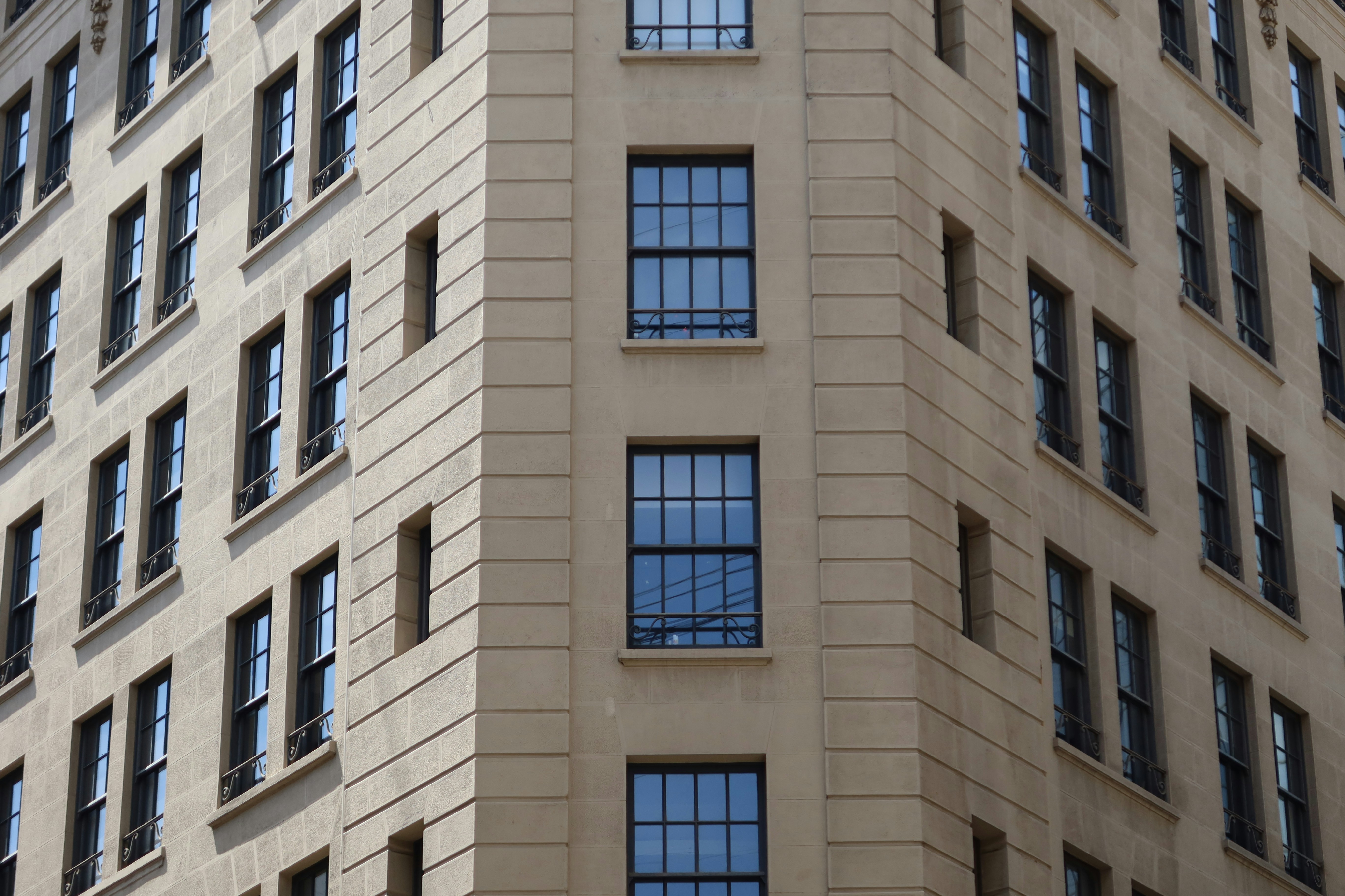 Corner of a beige stone building with symmetrical rows of windows under a cloudy sky.