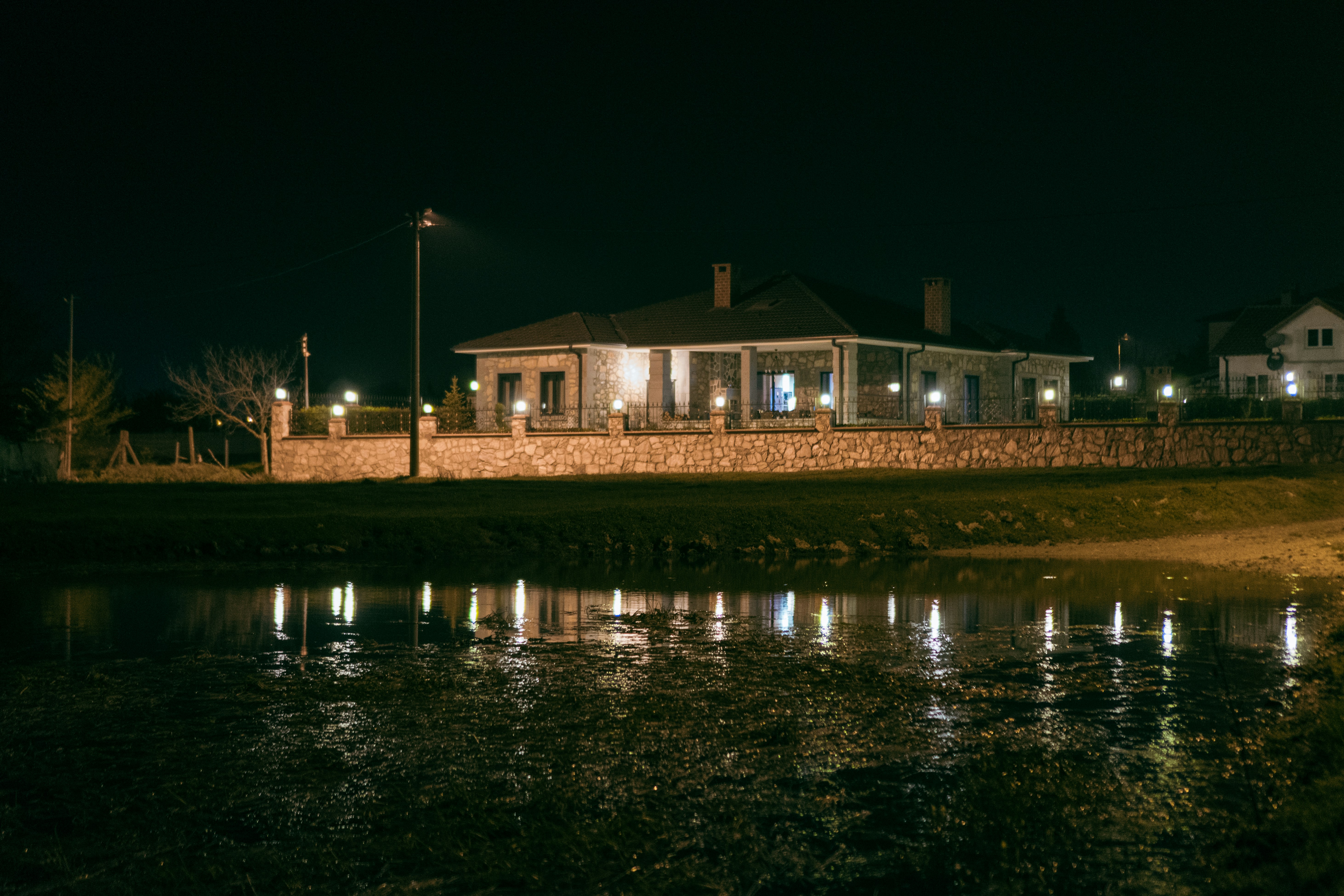 Cozy house with warm lighting reflecting on a calm river at night.