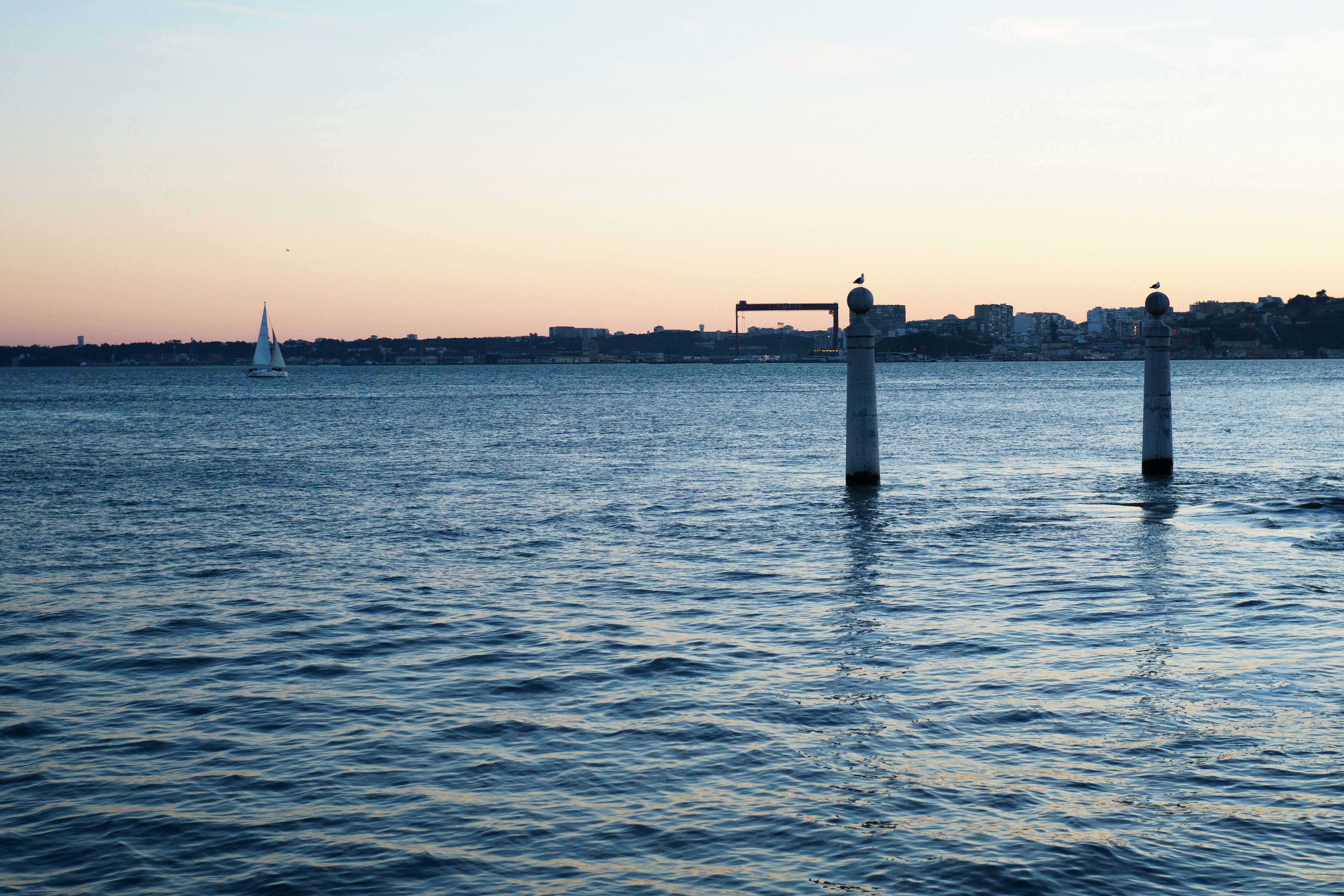 Calm waters at sunset with two columns in the foreground and a distant skyline on the horizon.