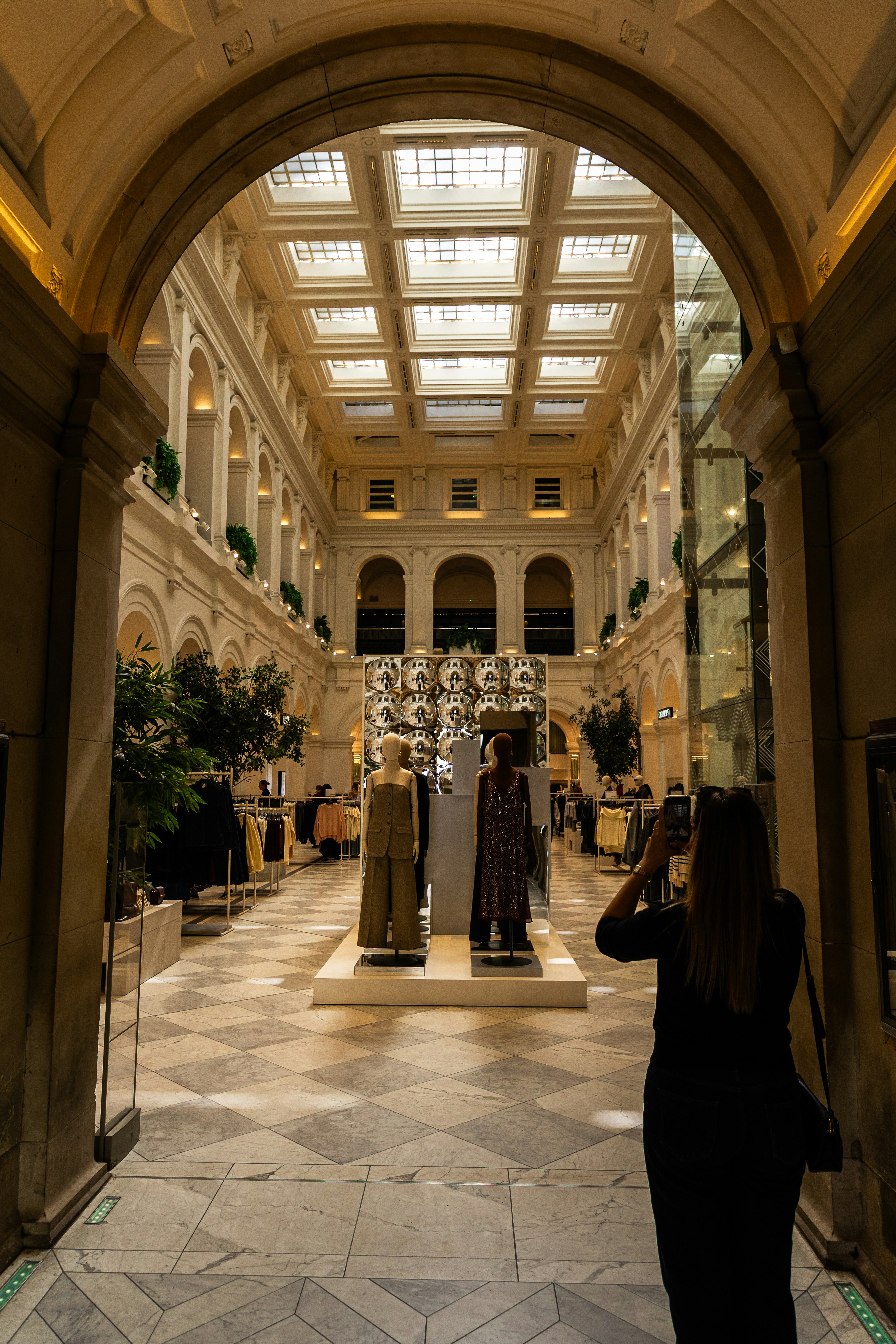 Woman photographs clothing displays in a grand hall. photo – Free Image ...