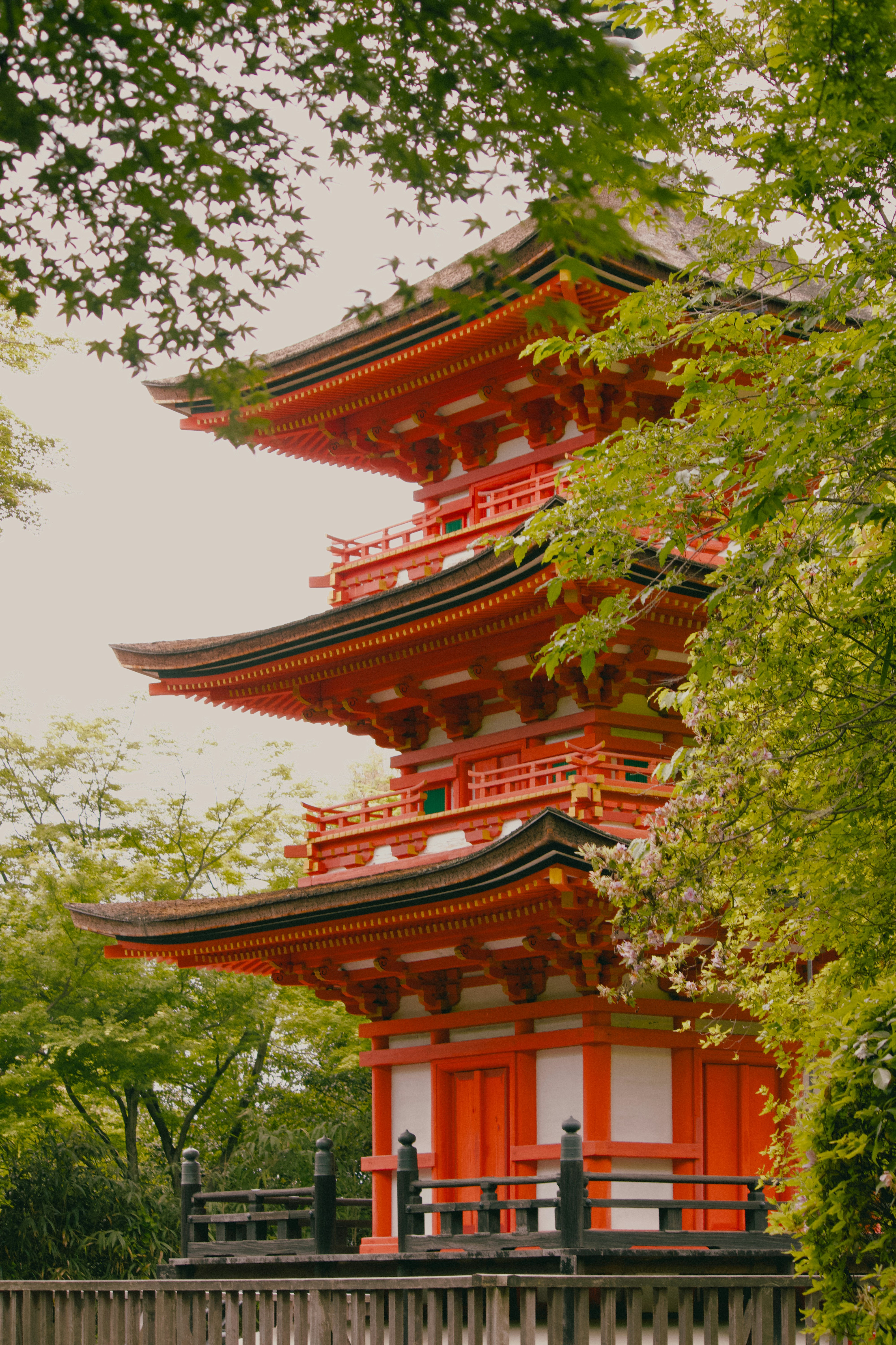 Traditional red pagoda surrounded by lush green foliage under a soft overcast sky.