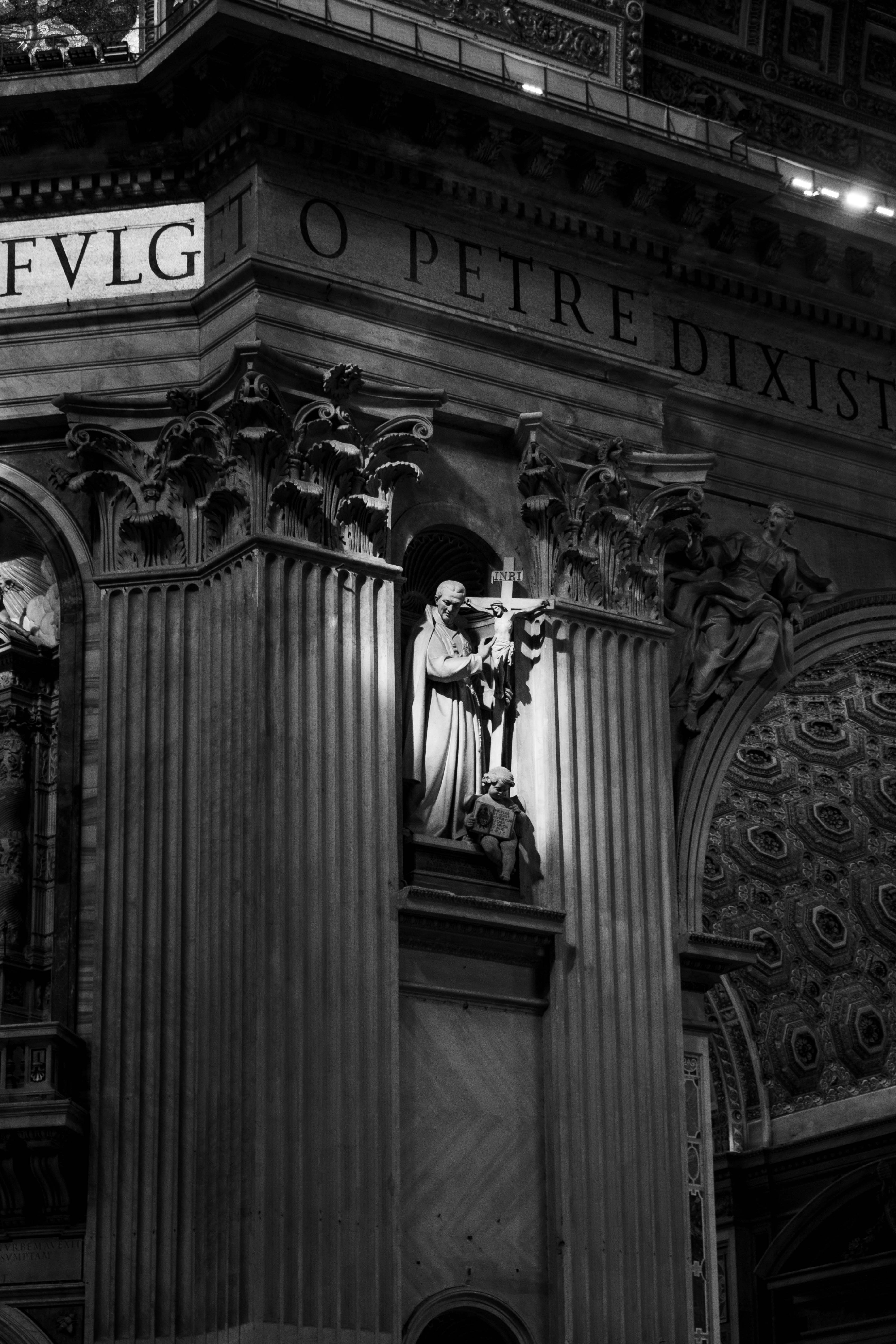 Monochrome architectural detail of a statue illuminated against ornate stone columns.