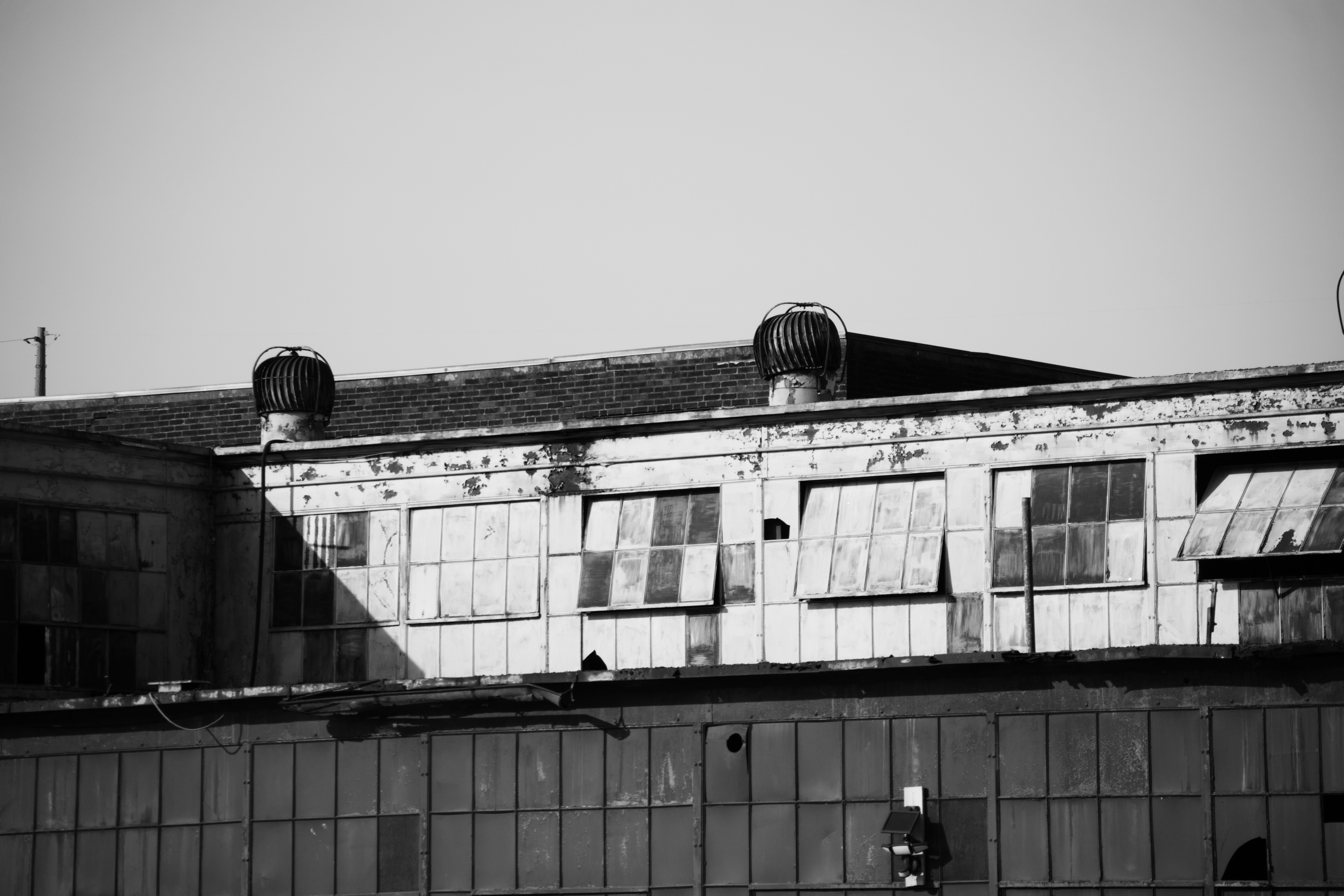 Black and white photo of a weathered industrial building with large, grid-like windows under a clear sky.