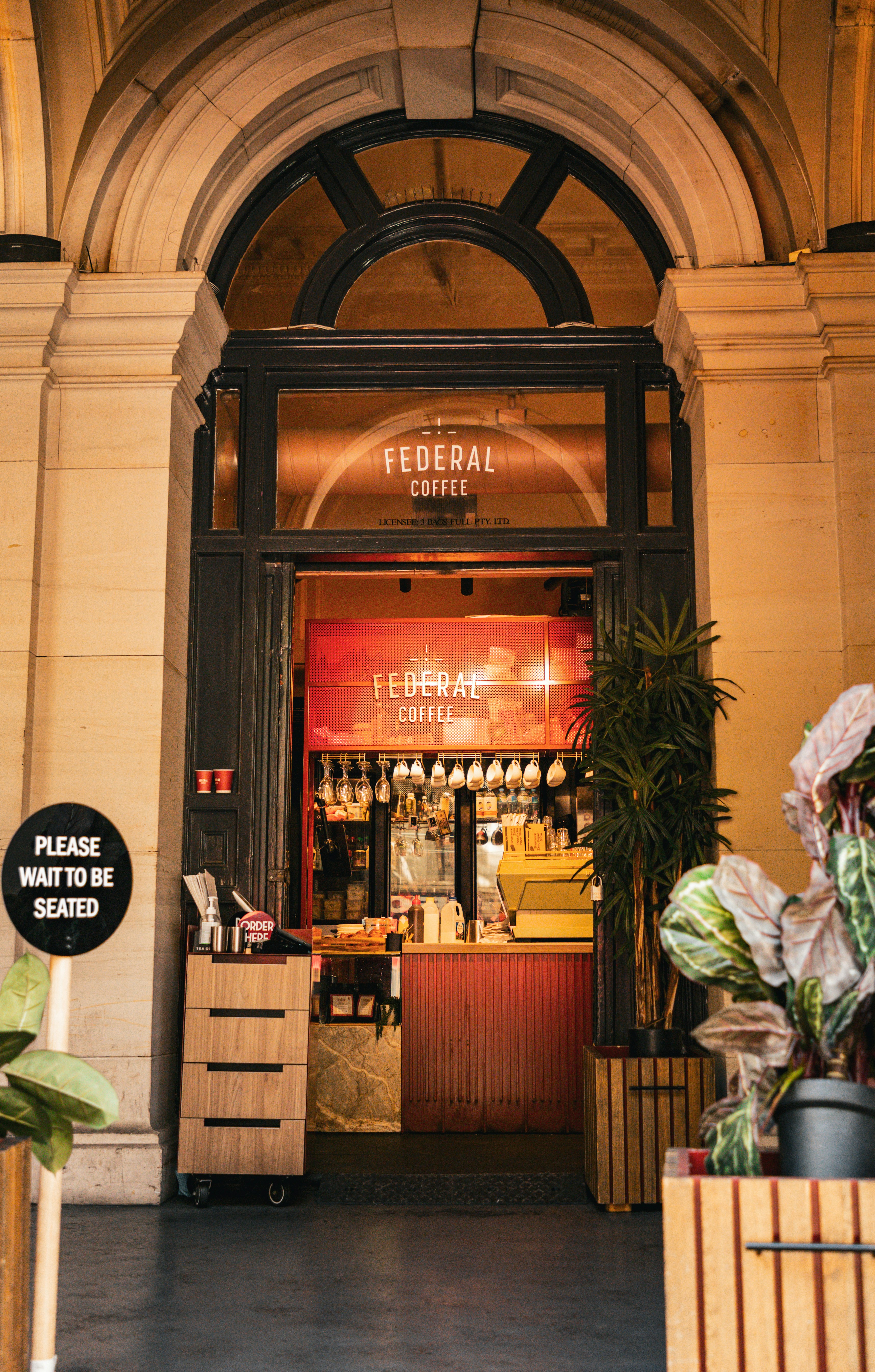 Charming coffee shop entrance with a vibrant red interior and a sign requesting patrons to wait to be seated.