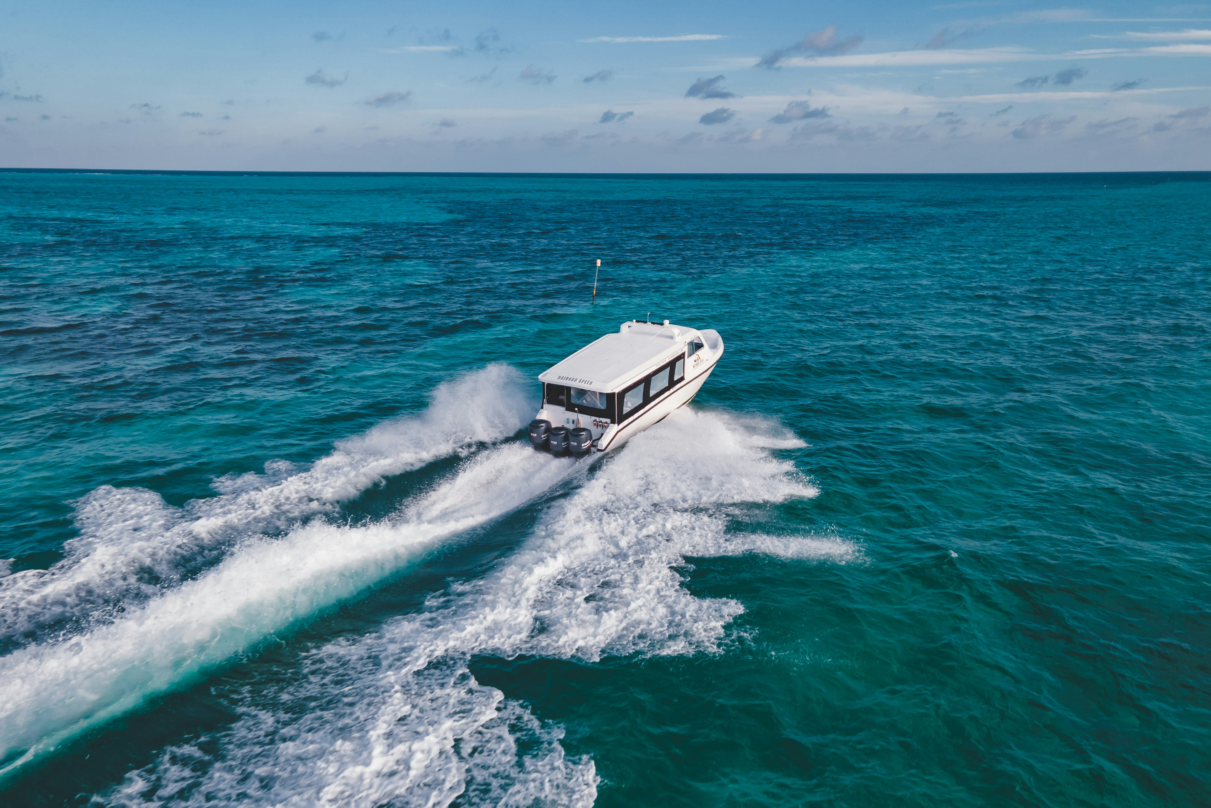White motorboat speeds through turquoise waters, leaving a dynamic wake against the horizon under a cloud-streaked sky.