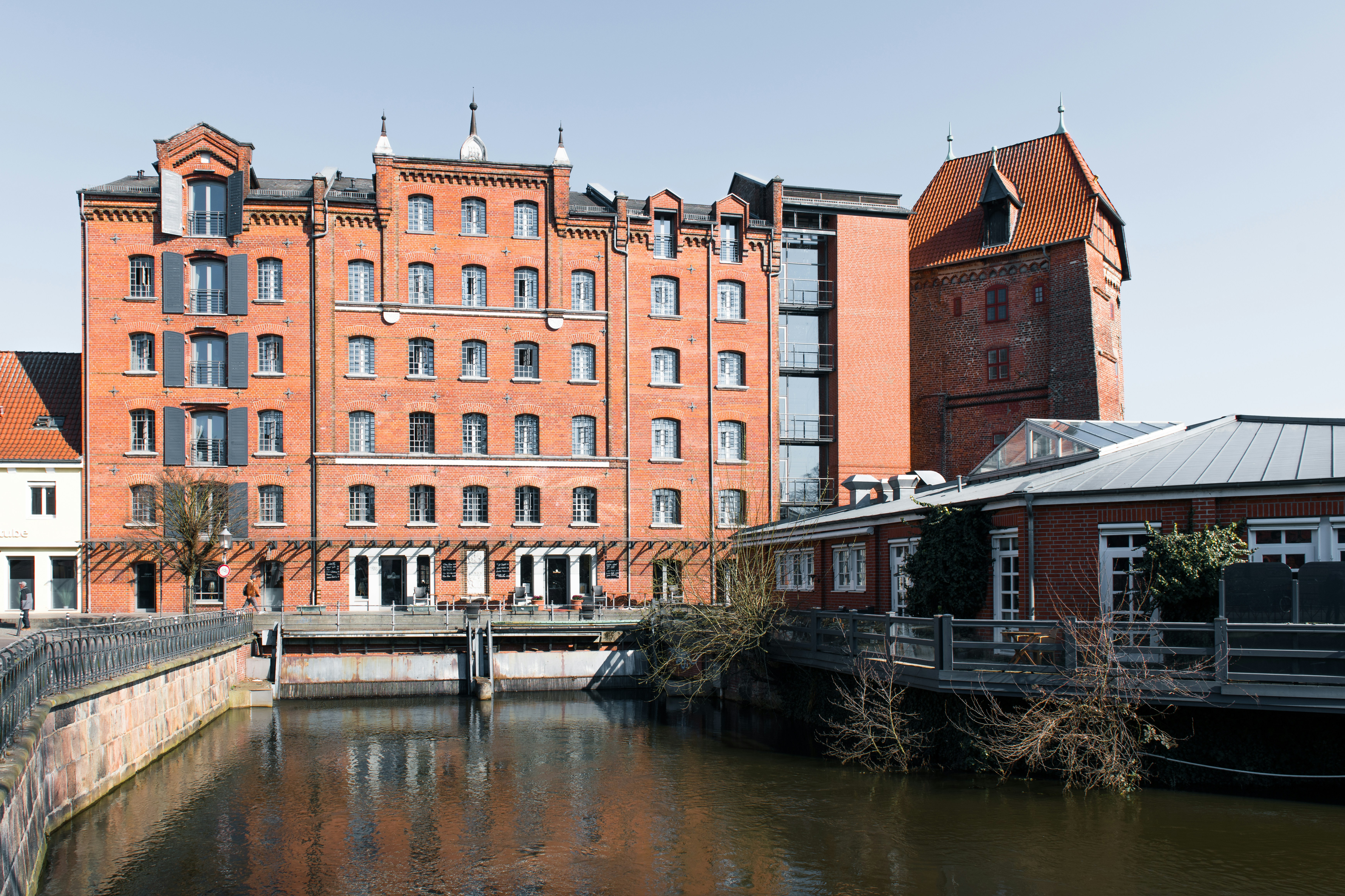 Red brick building reflecting in a calm canal under a clear blue sky.