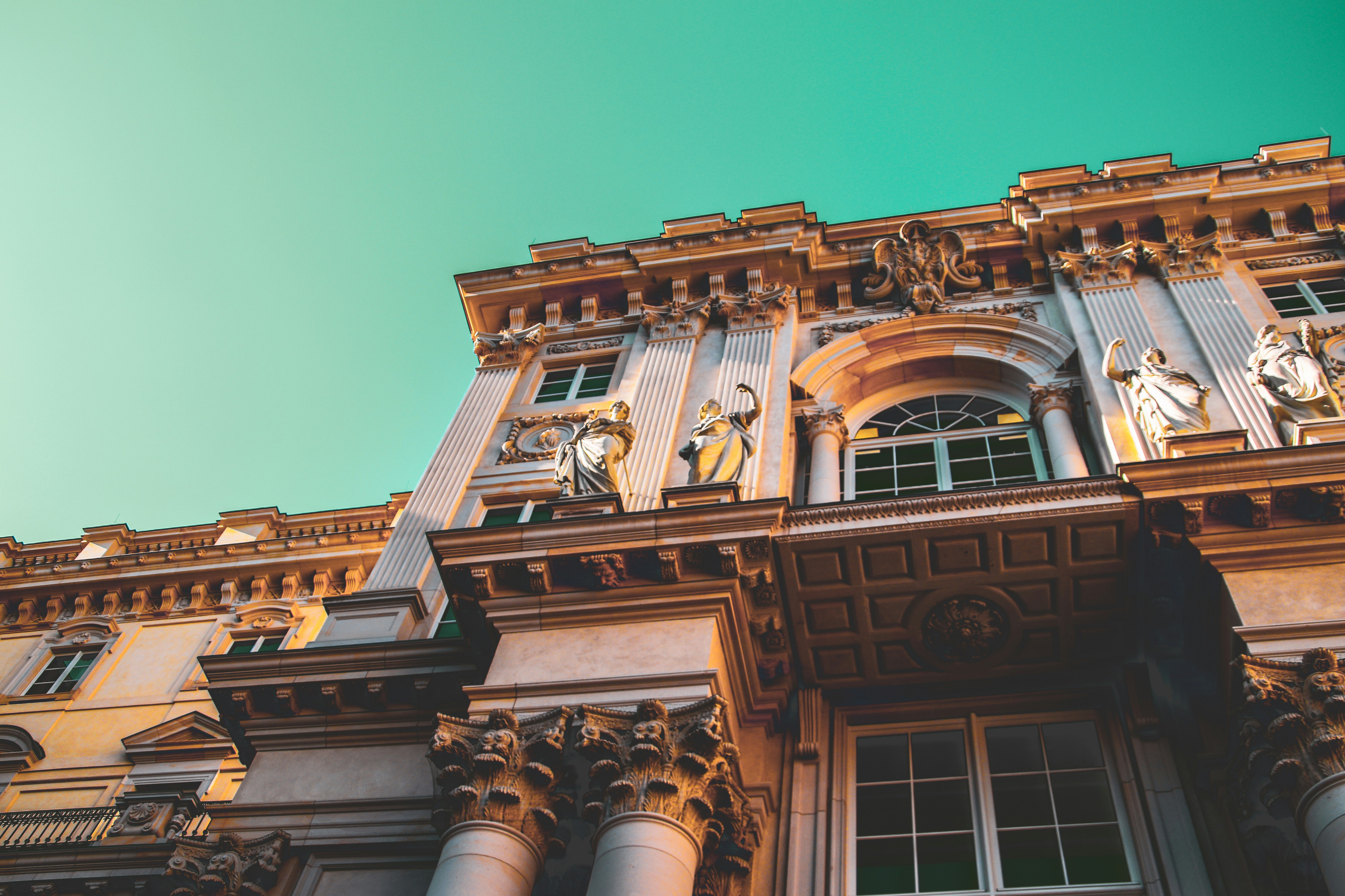 Ornate architectural facade with statues and columns set against a vibrant turquoise sky.