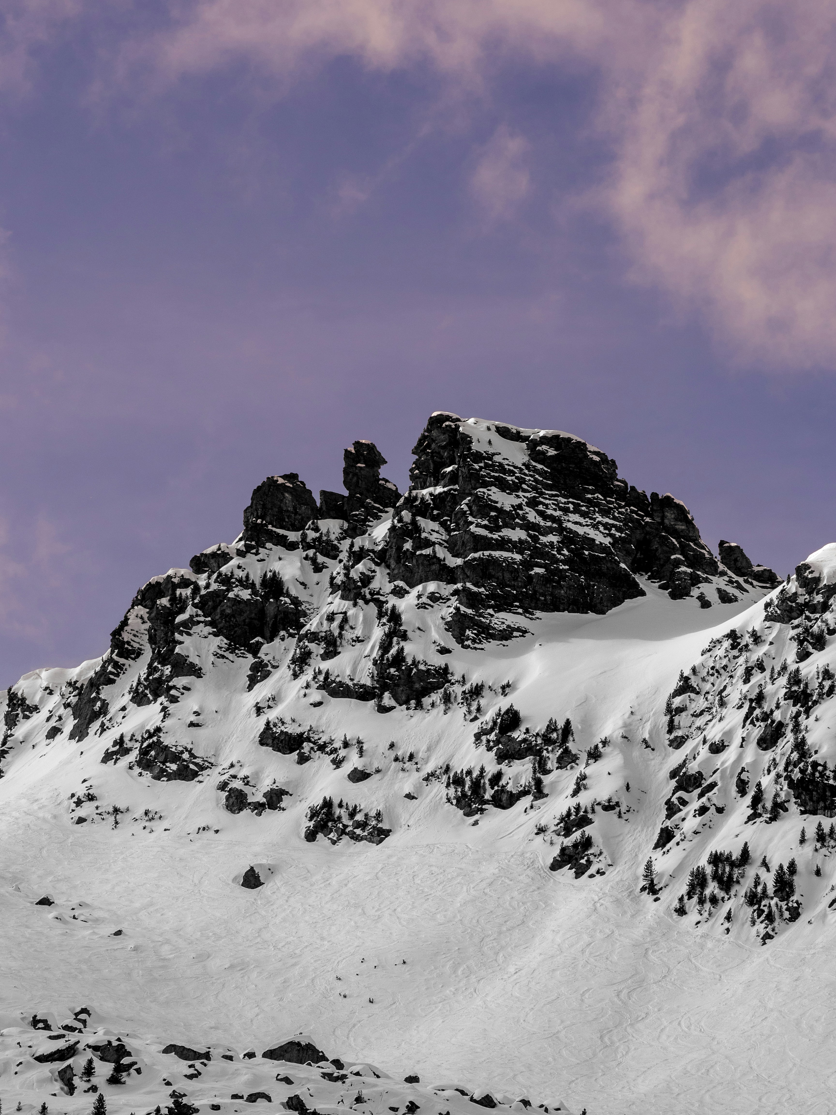 Snow-covered rocky mountain peak under a lavender-tinted sky.