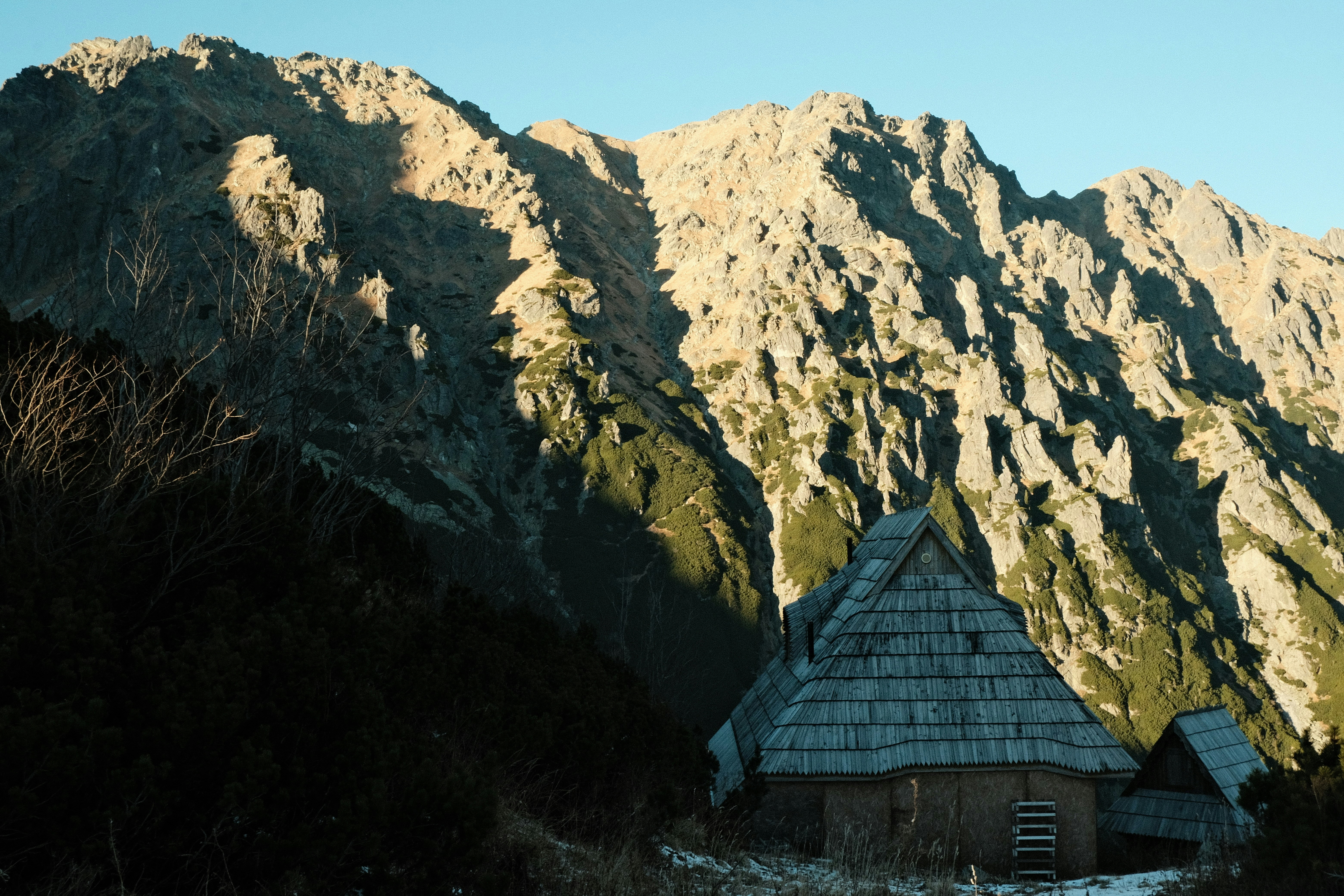 Foot of the Peaks: A Weathered Alpine Cabin Clinging to Rugged Cliffs