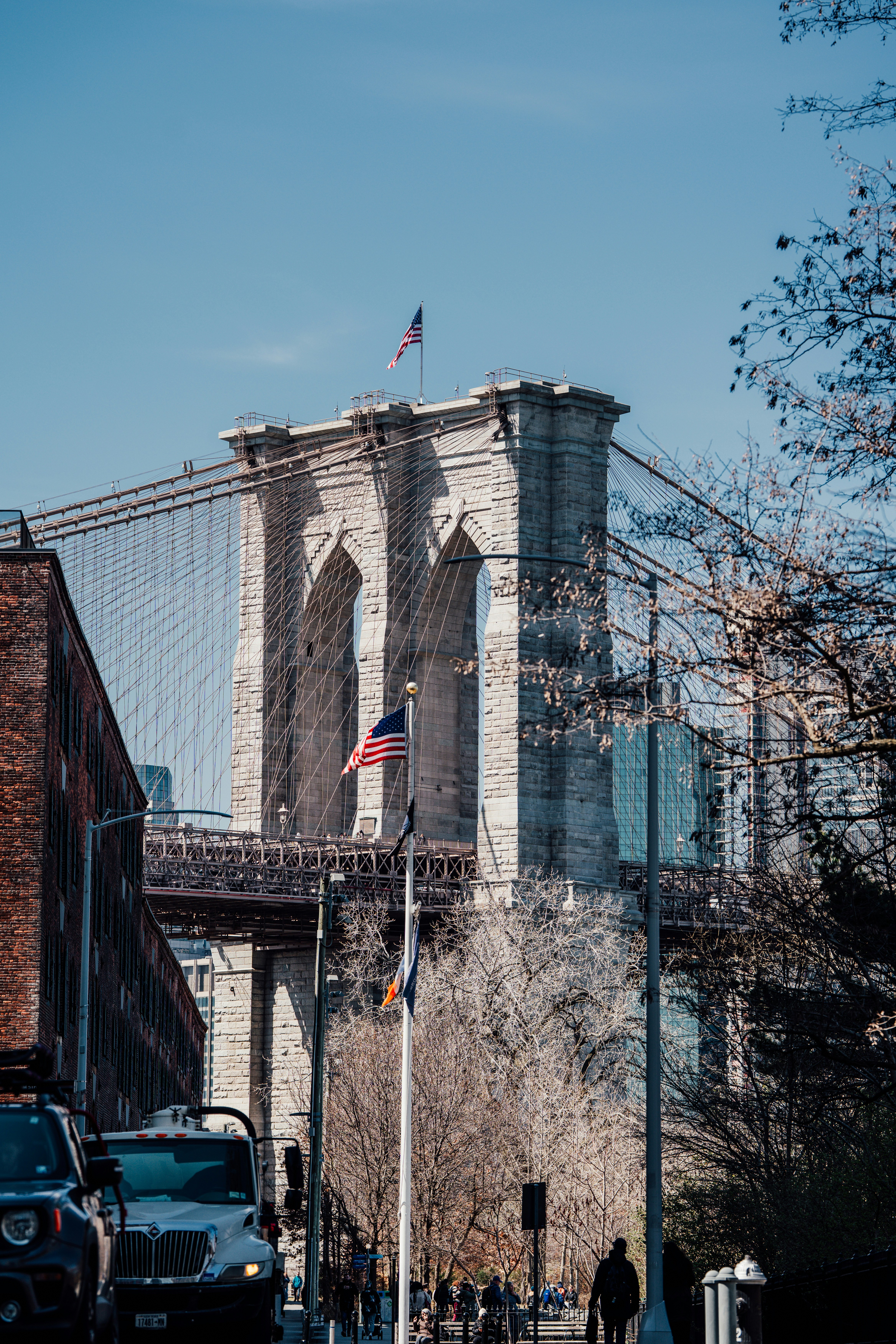 Brooklyn Bridge towers framed by city buildings under a clear blue sky.