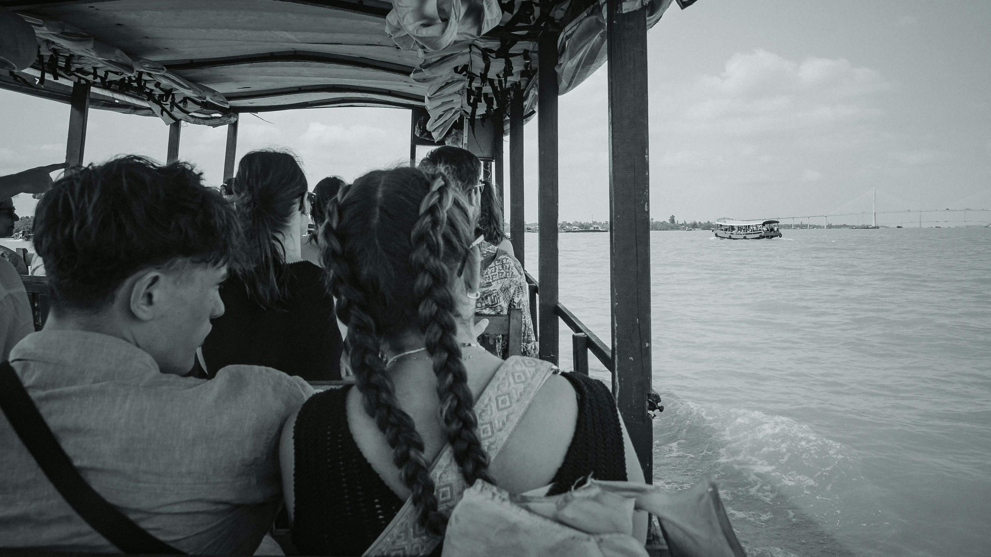 Passengers seated on a boat glancing at the serene river under a bright sky.