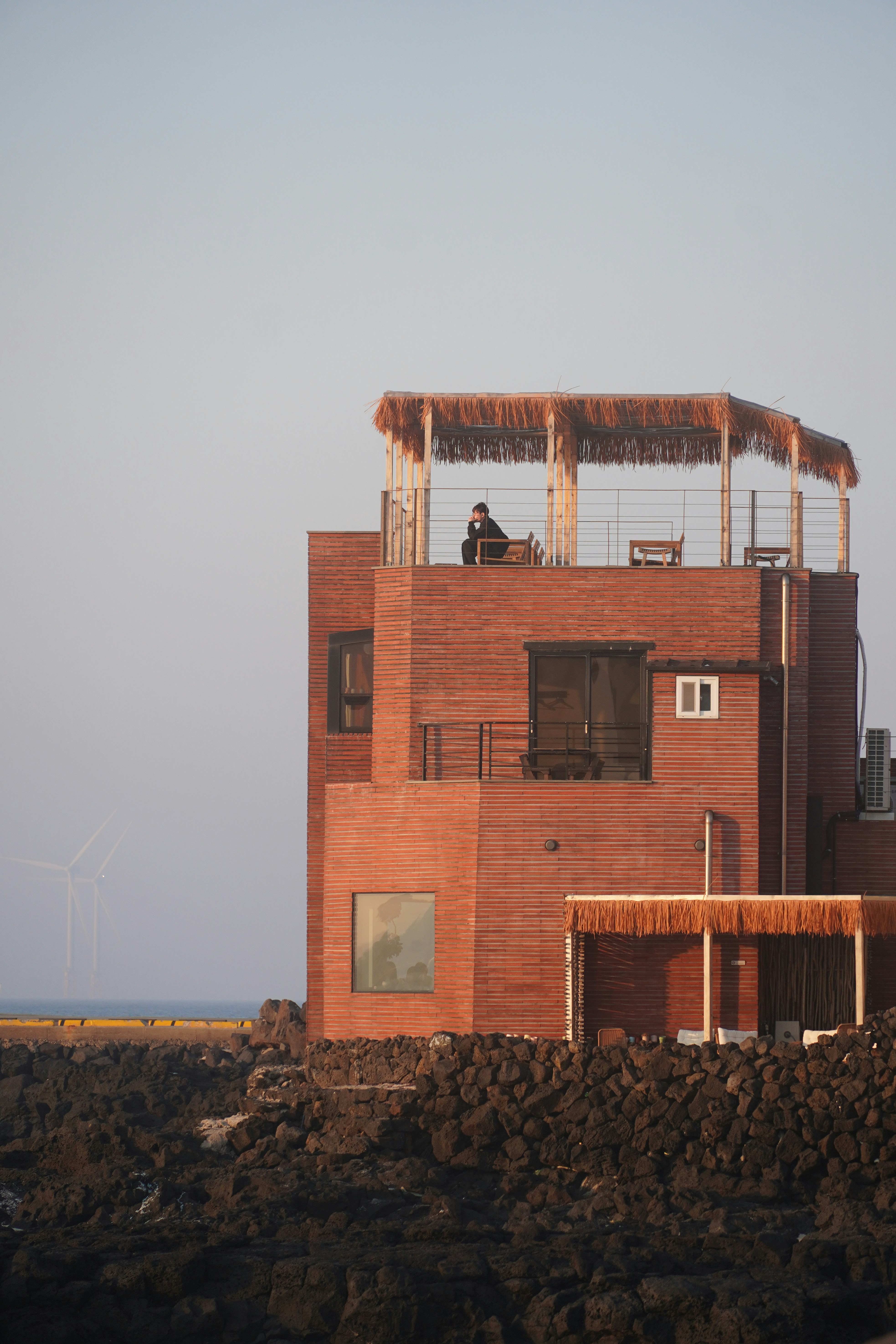 Rooftop Watcher: A Lone Figure on a Brick Coastal Tower
