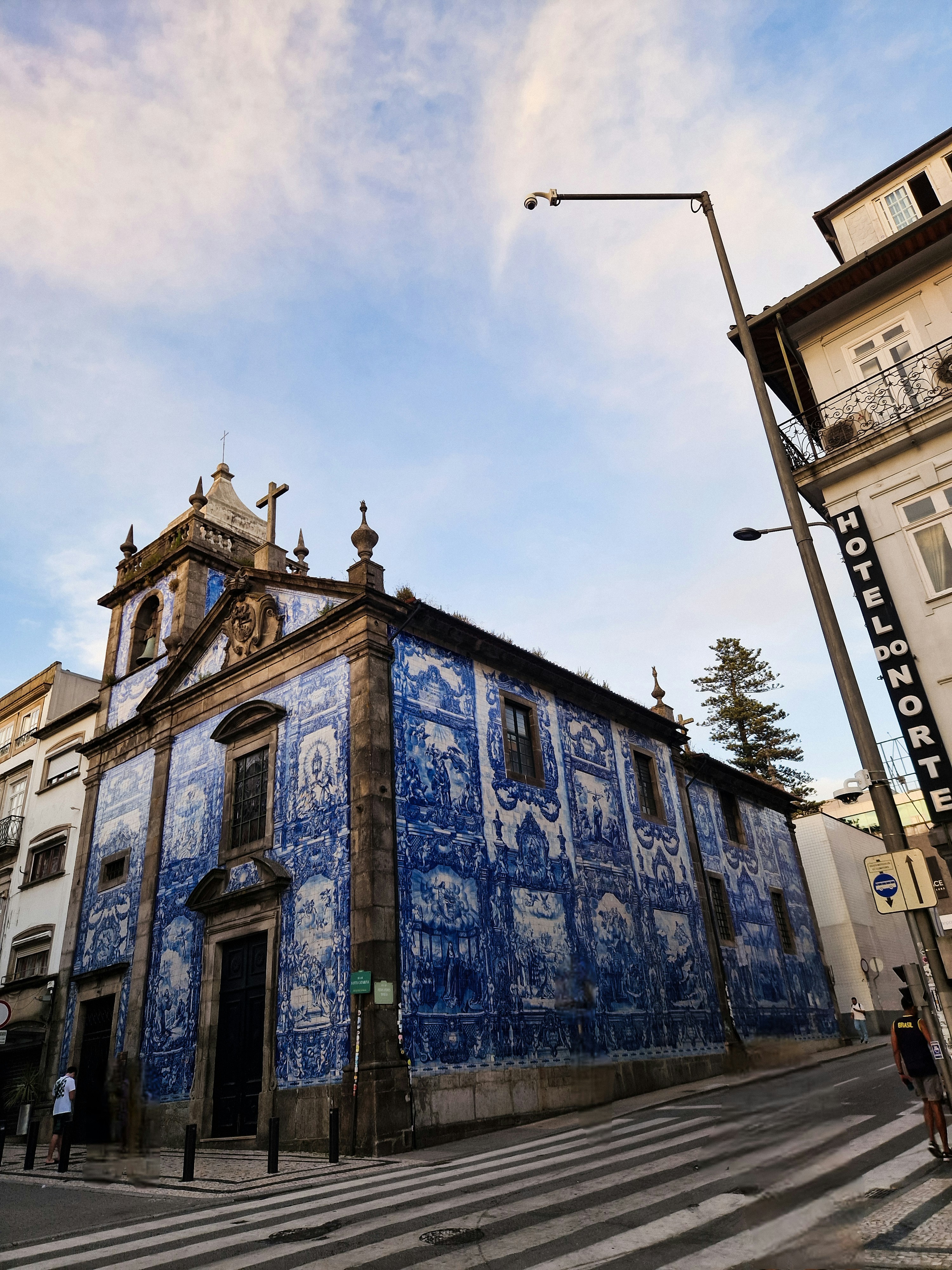 Church adorned with intricate blue azulejos under a vibrant sky, adjacent to modern buildings.