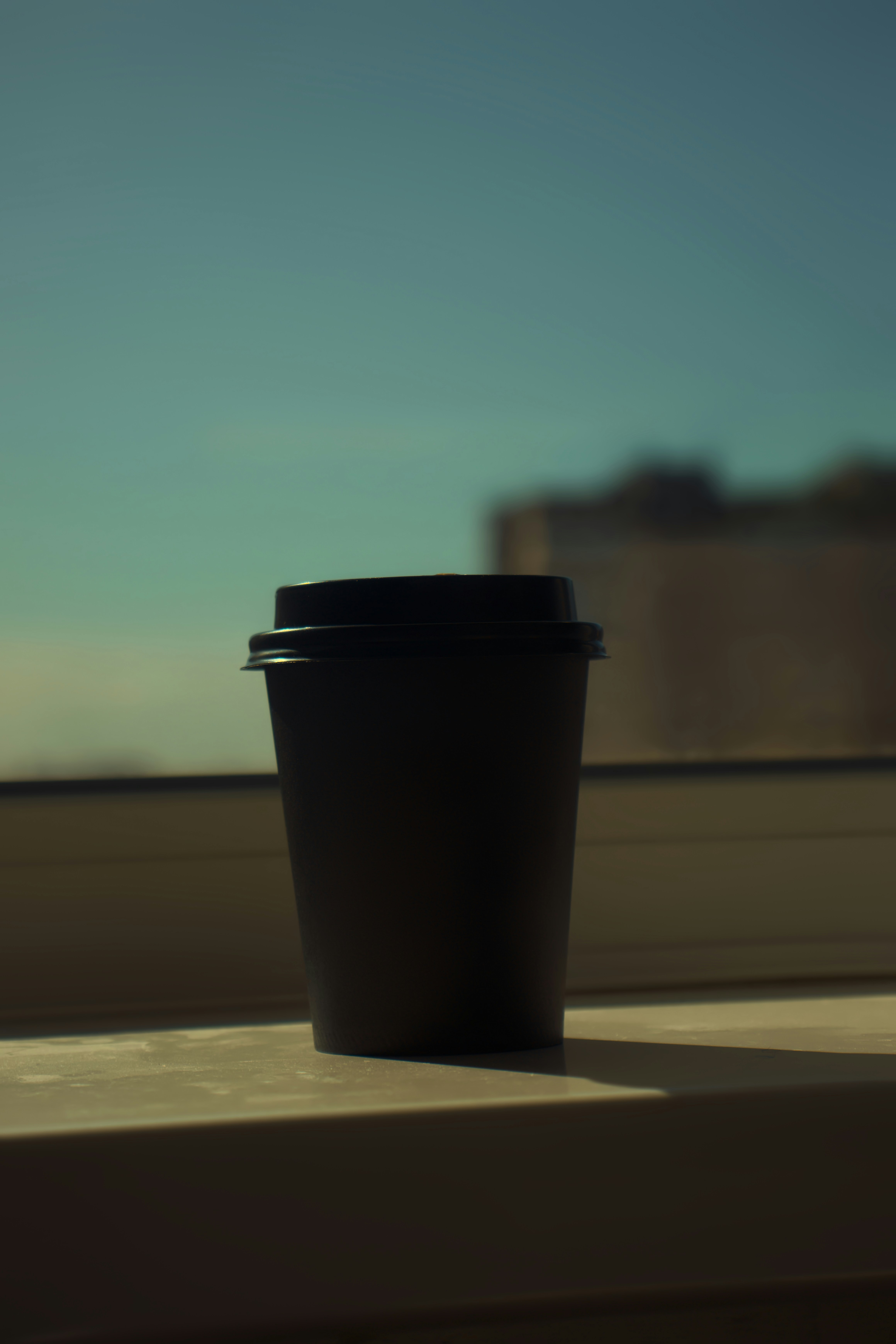Centered take-away cup on a sunlit rooftop ledge beneath a turquoise sky gradient