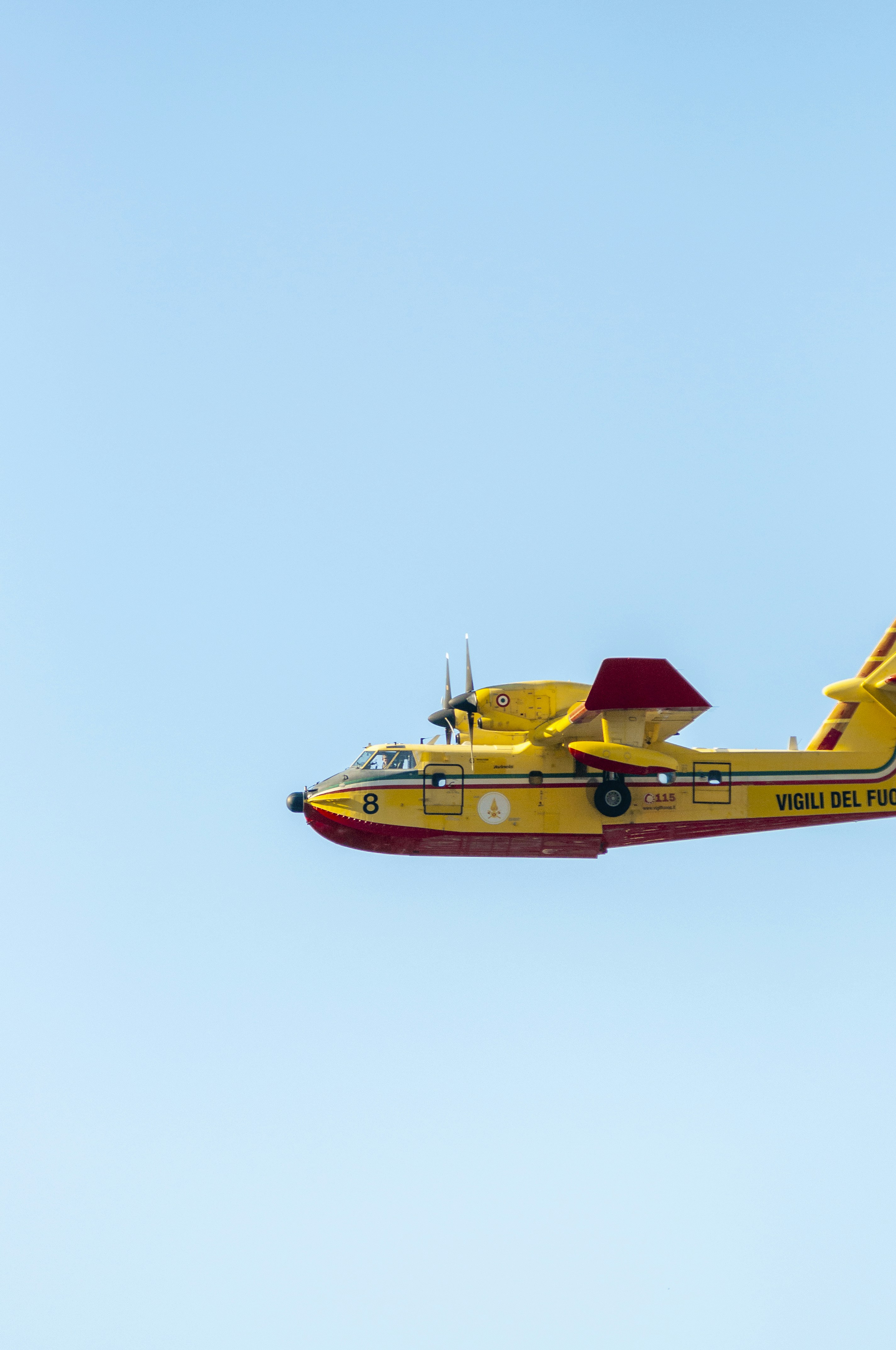Yellow Canadair aircraft soaring against a clear blue sky.