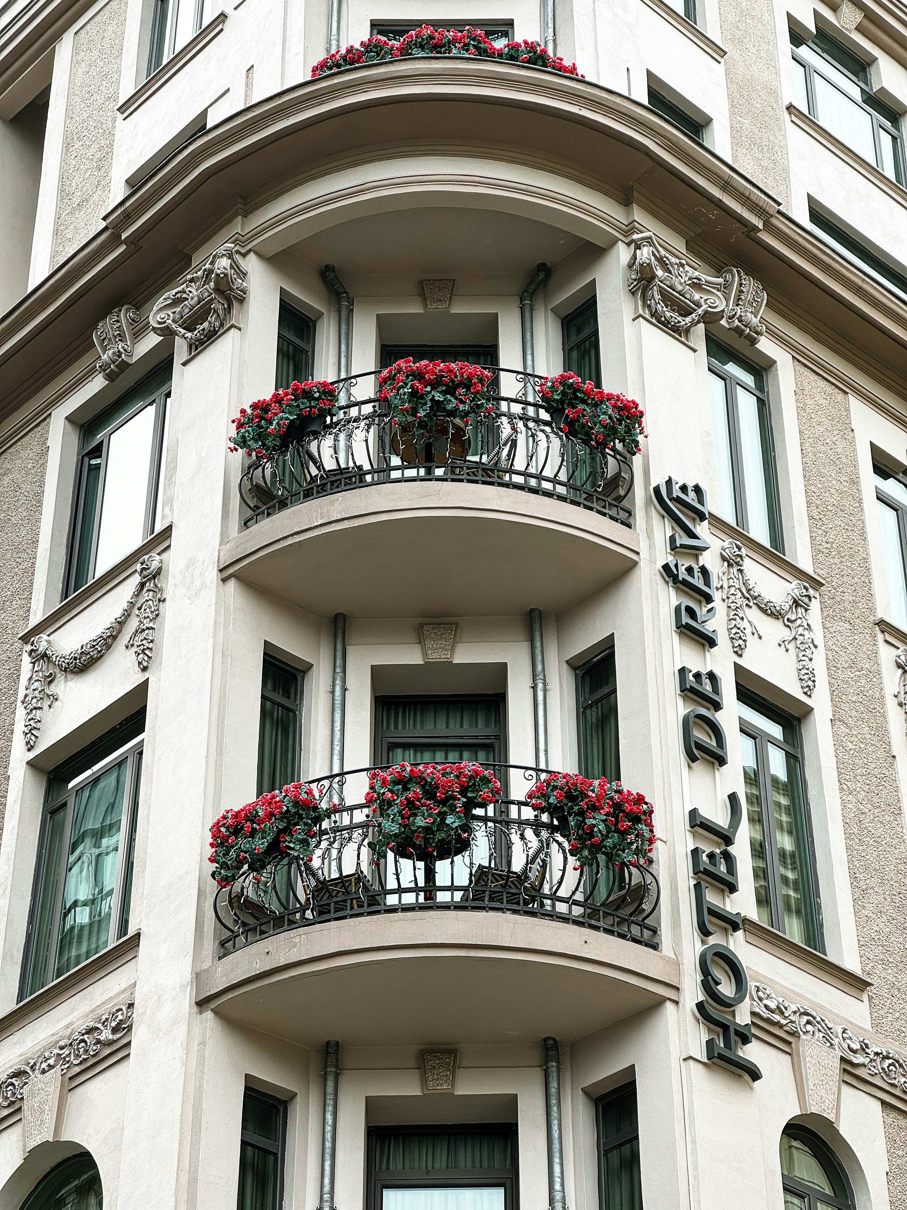 Art Nouveau hotel façade with ornate balconies adorned with vibrant red flowers.