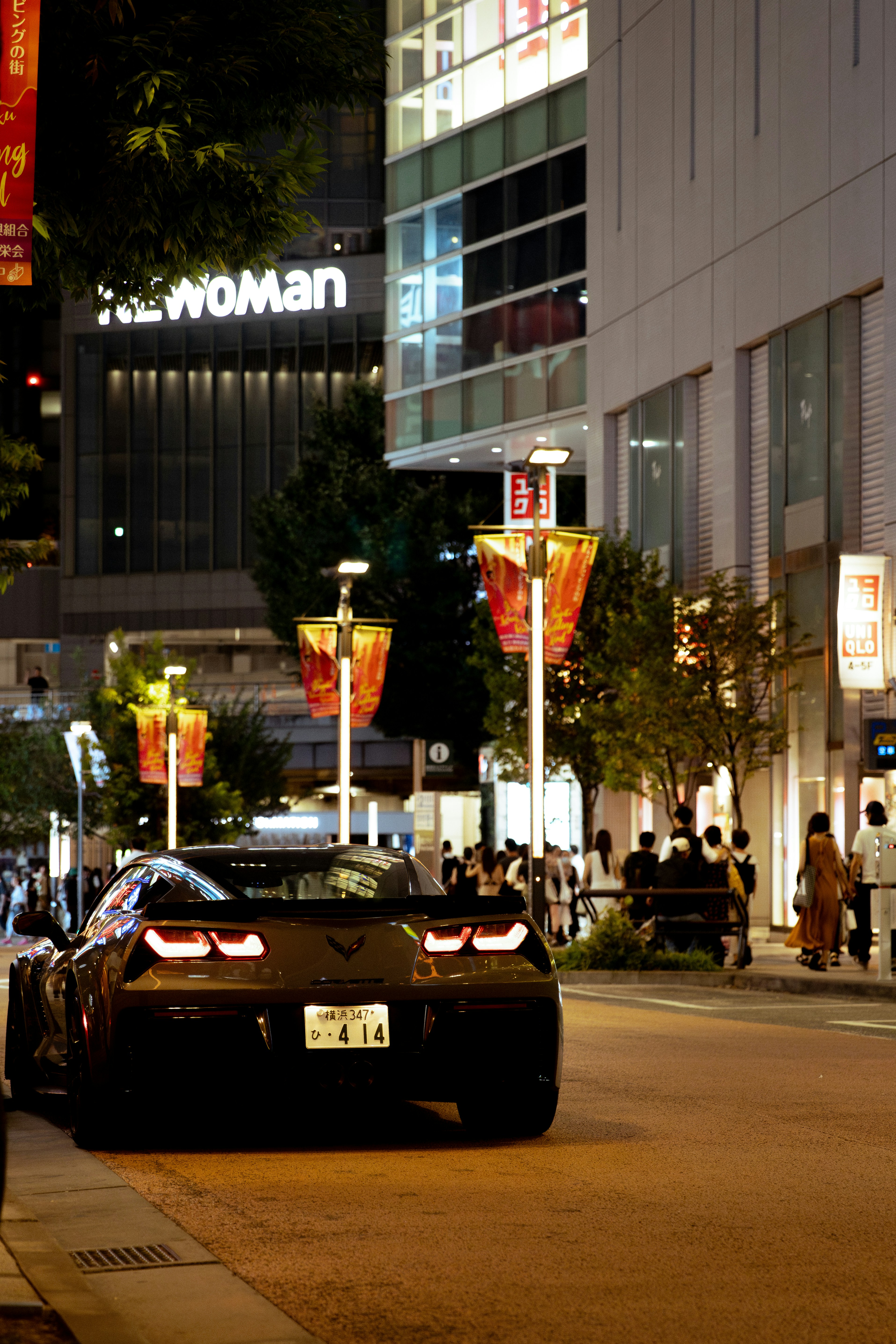 Midnight Corvette Beneath Neon: Quiet Pause on a Bustling Street