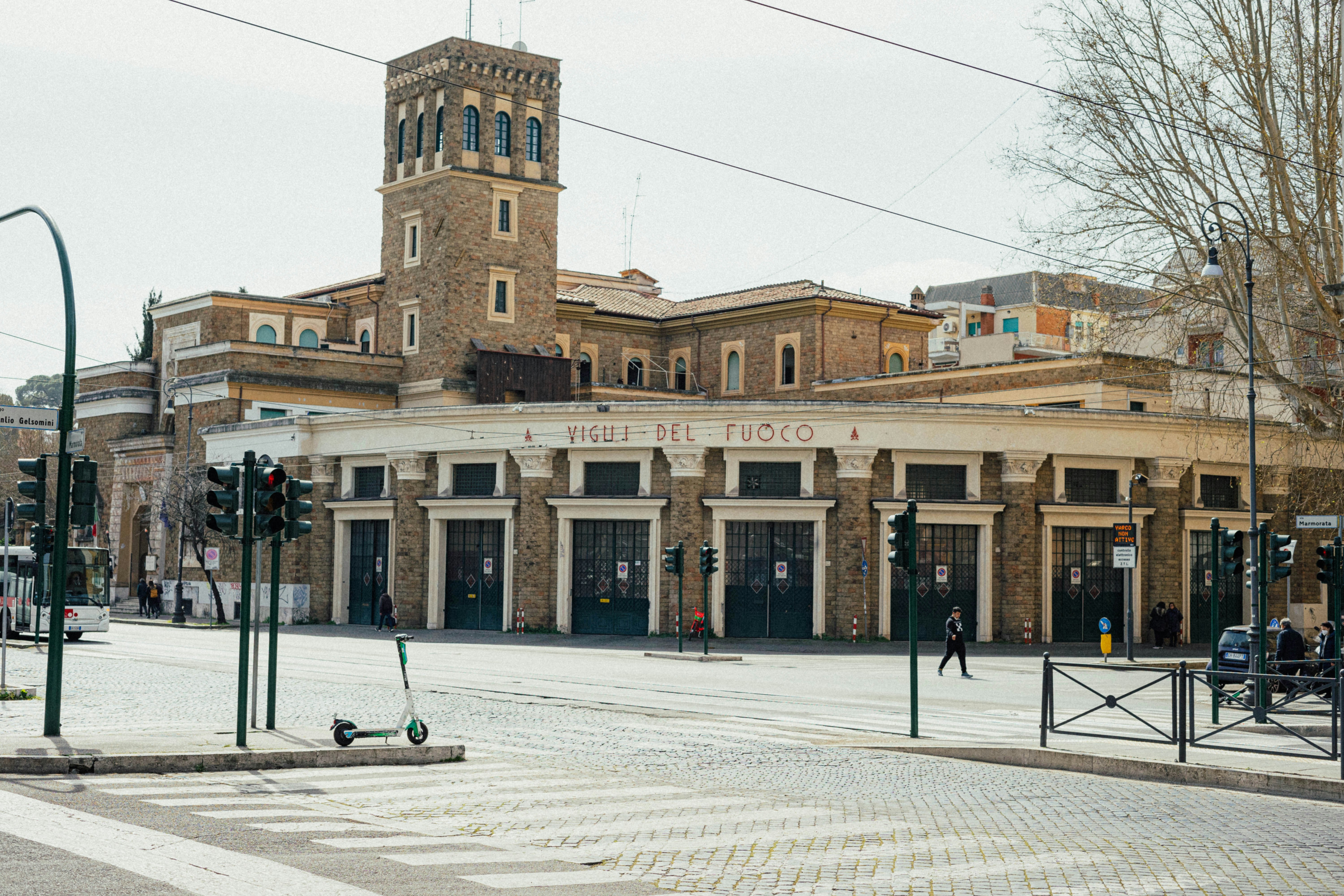 Historic building with tall tower and arched doorways on a deserted street corner under overcast sky.