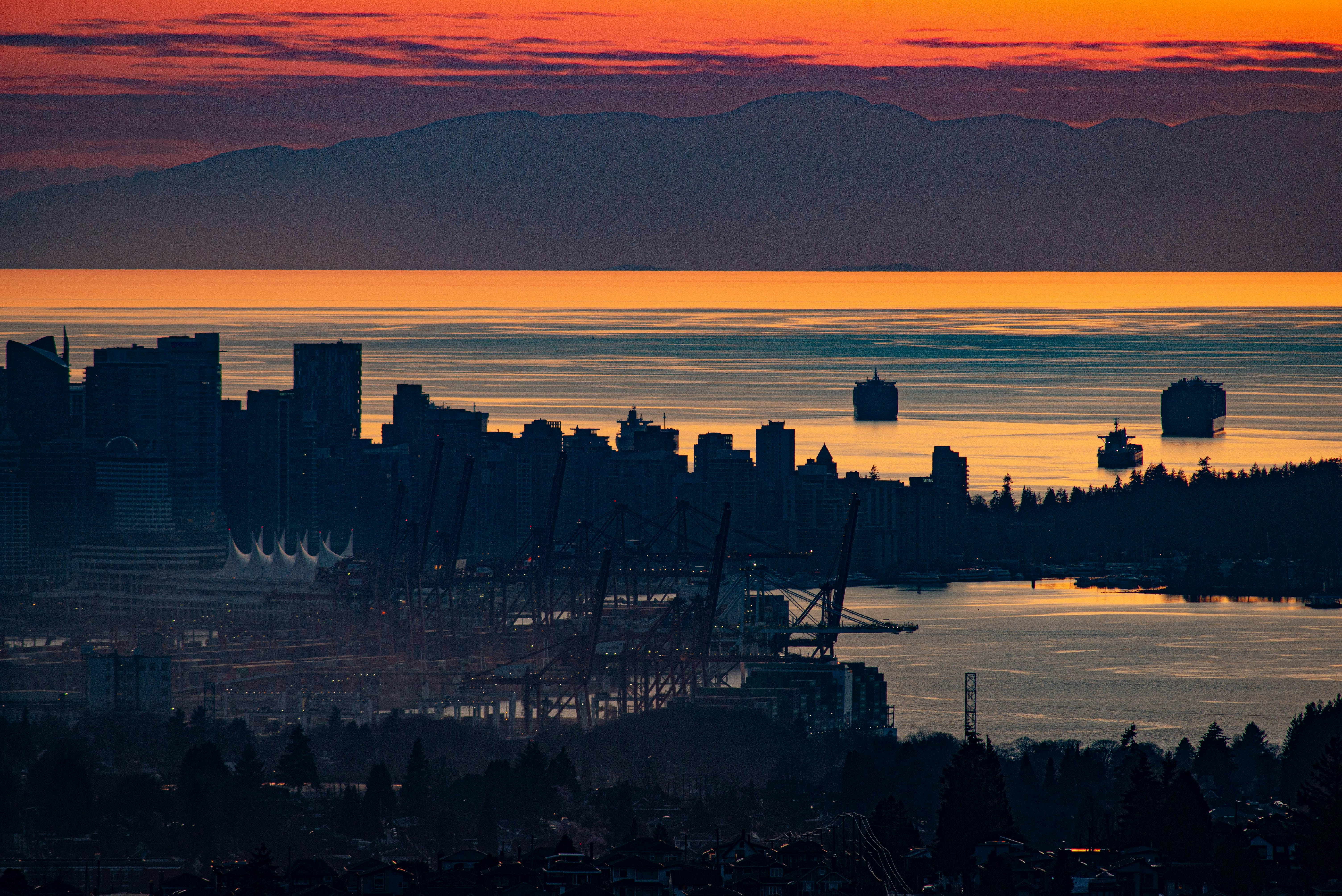 Silhouetted port facilities and cityscape against a vibrant sunset sky from Burnaby Mountain Park.