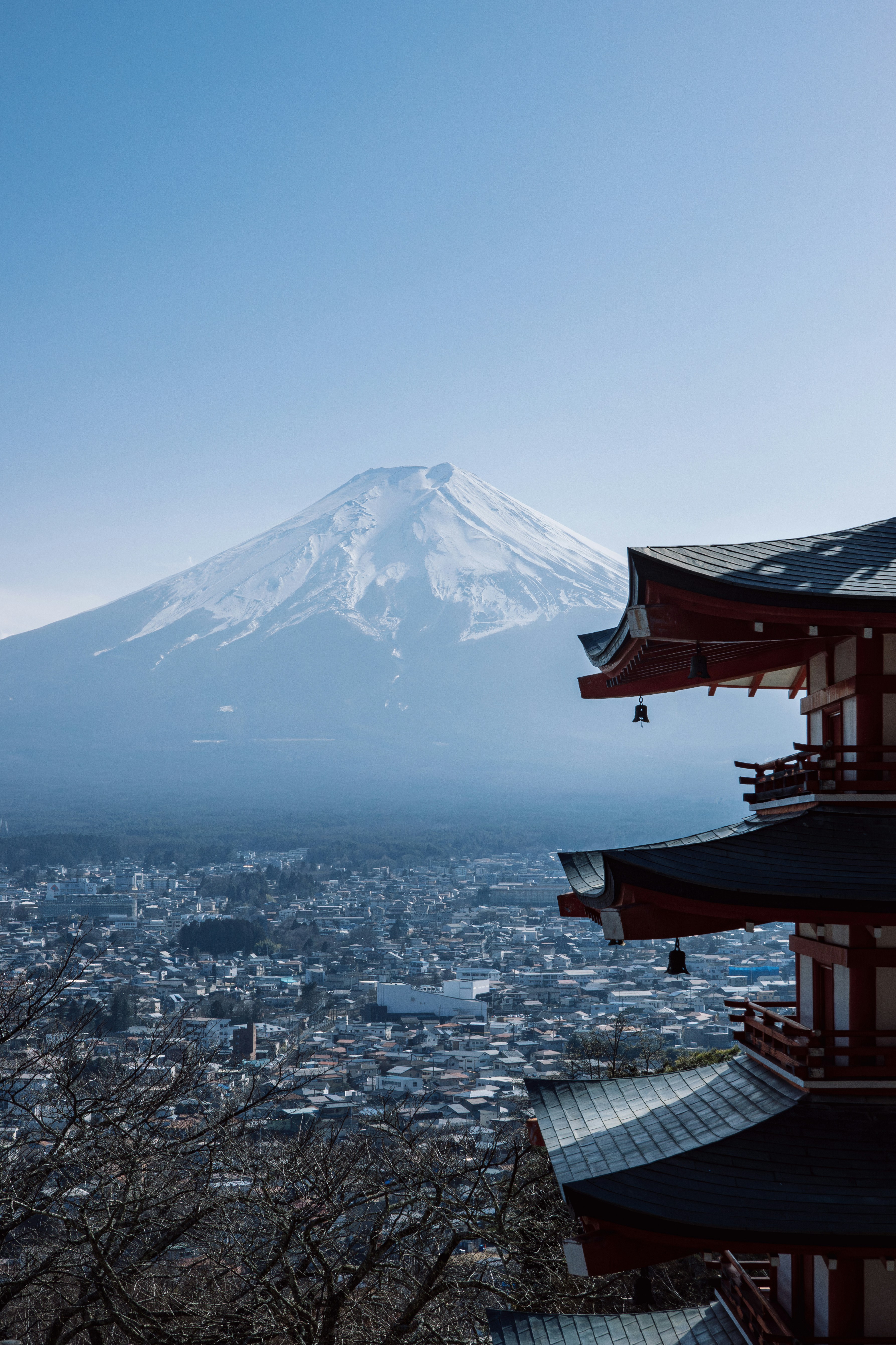 Mount Fuji framed by a traditional pagoda overlooking a sprawling cityscape under a clear blue sky.