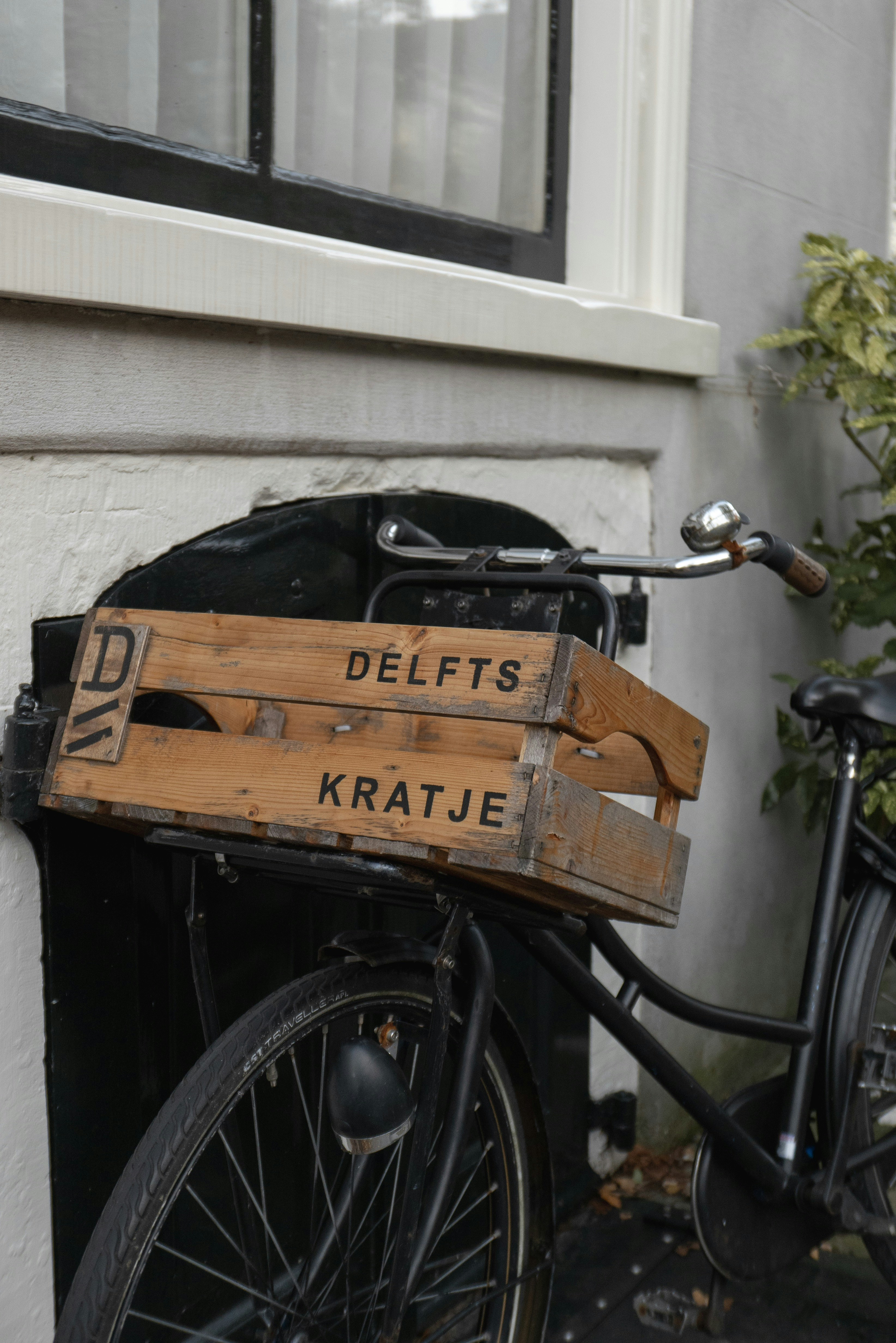 Vintage bicycle with a wooden crate marked 'Delfts Kratje' leaning against a building.