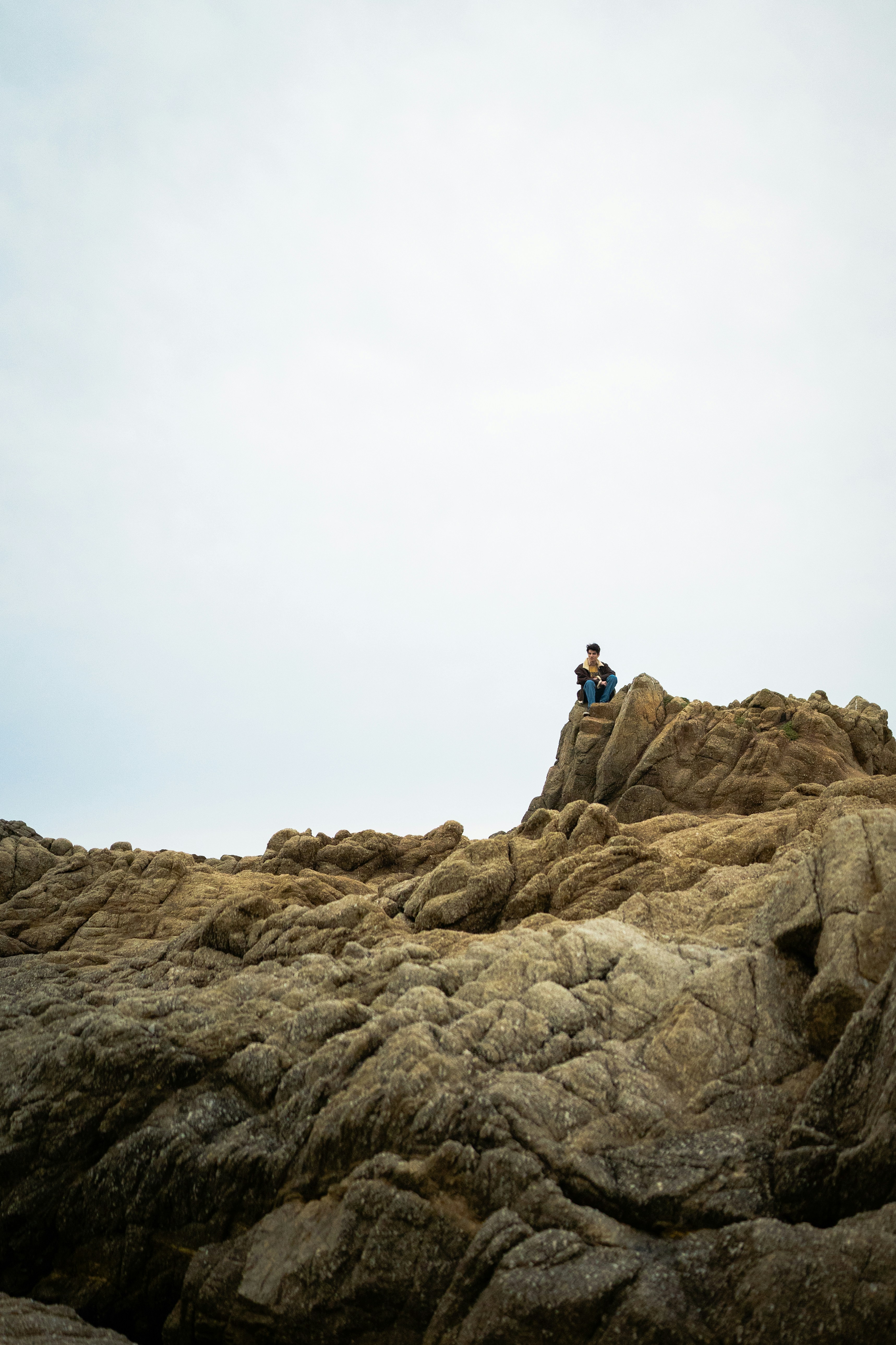 Person standing atop large, weathered rocks under an expansive sky.