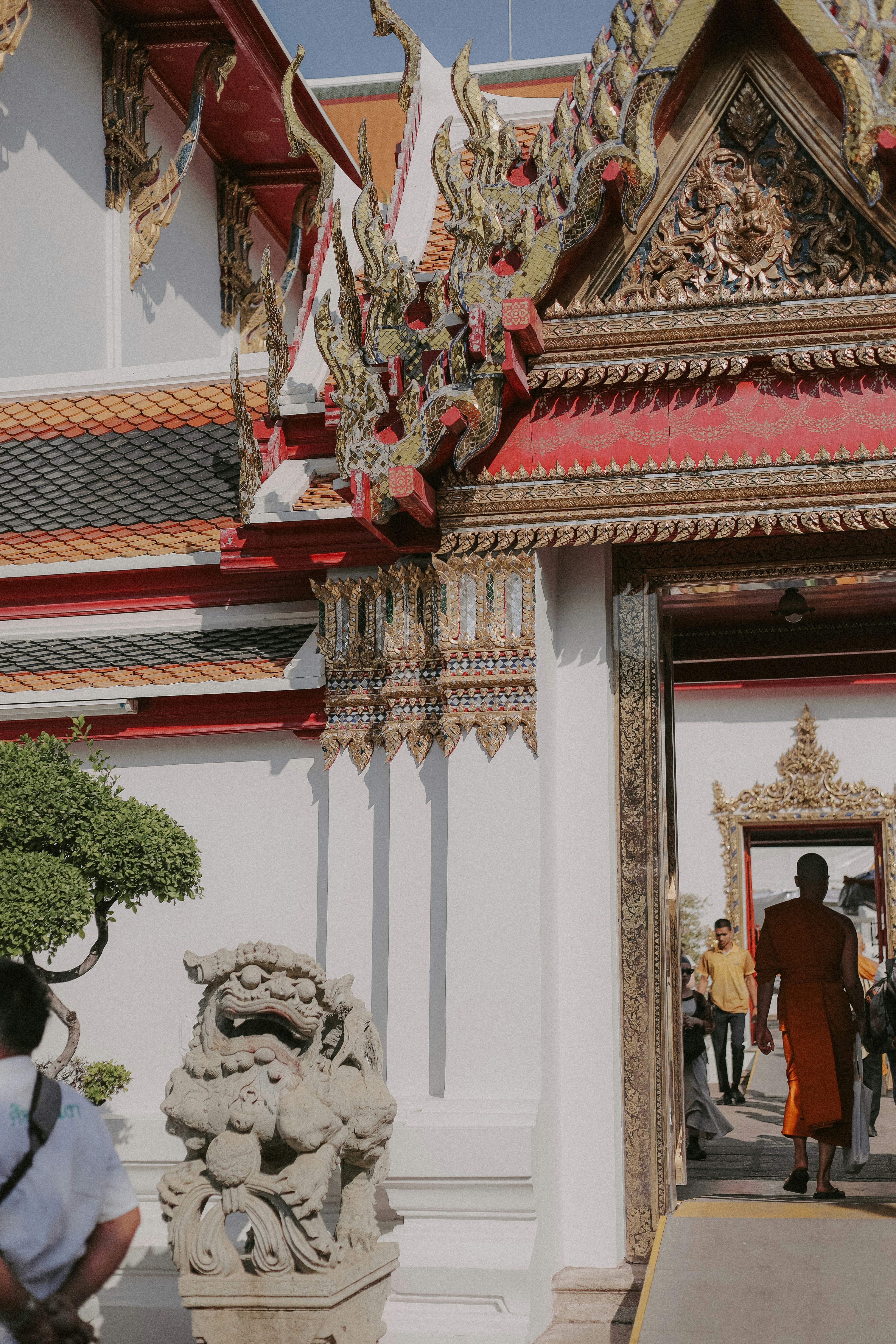 Intricate temple entrance adorned with gilded details and a stone guardian statue under clear skies.