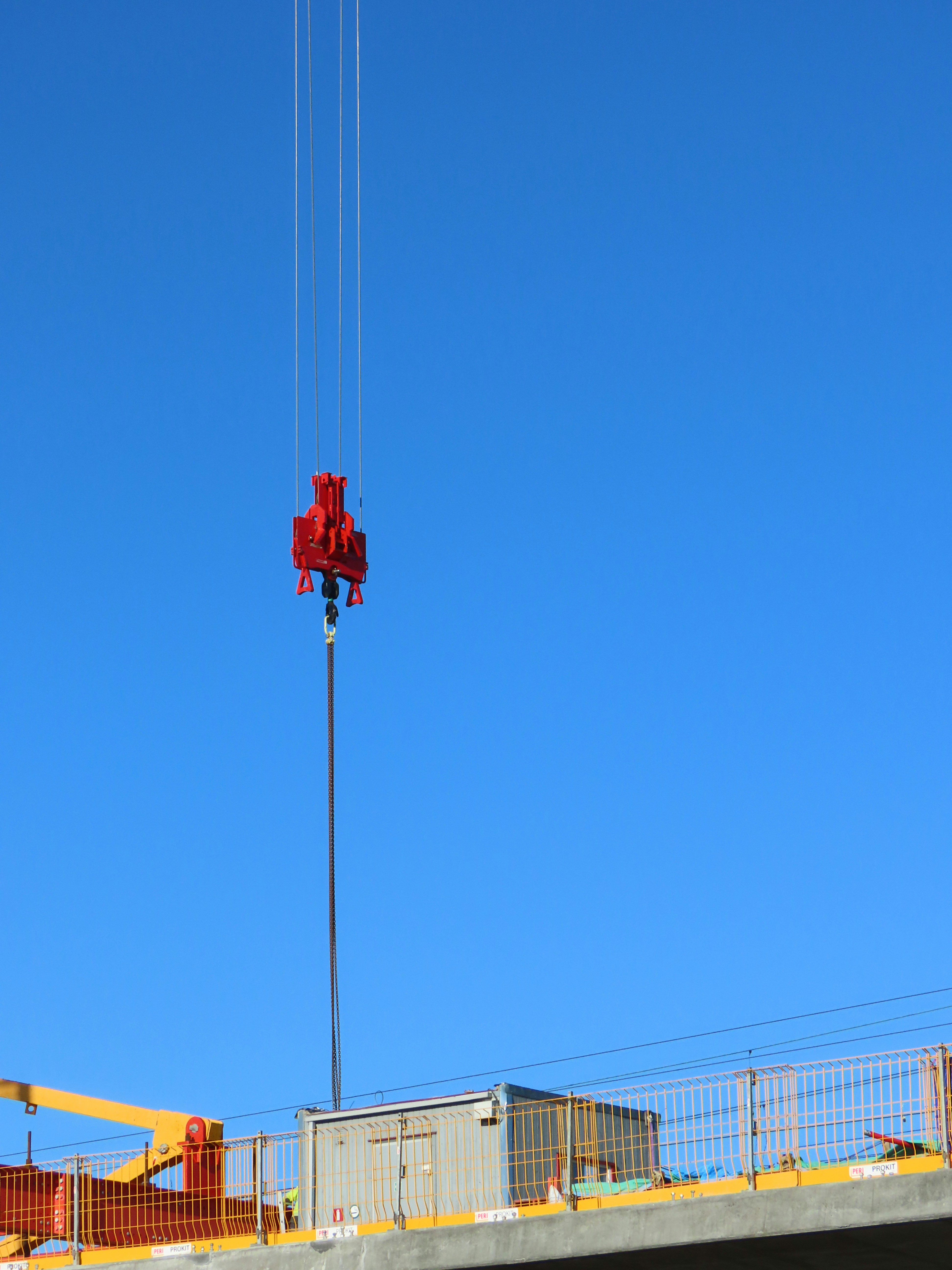 Crimson Lifting Clamp Hovering Over a Construction Platform Against a Clear Blue Sky