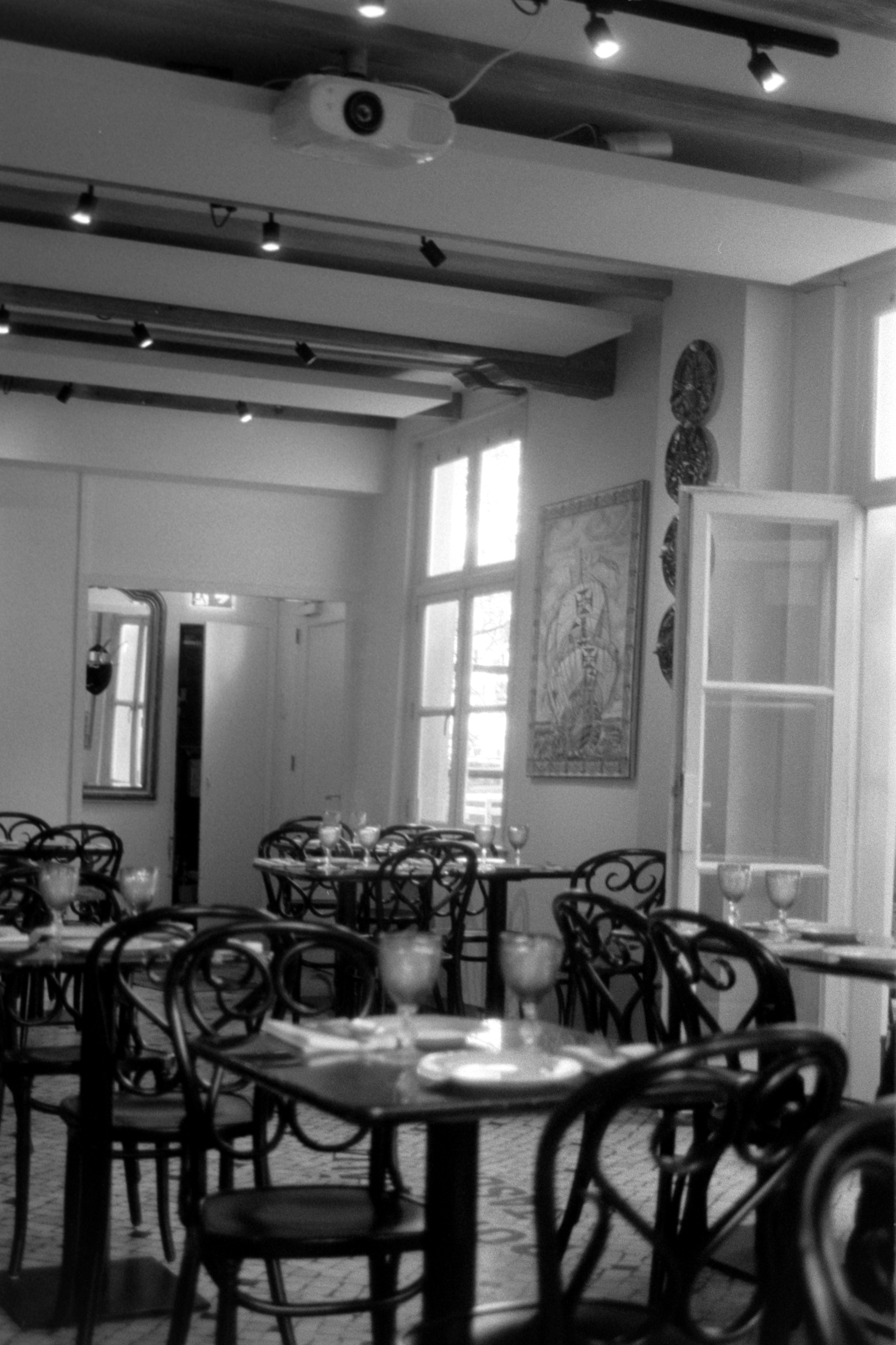 Black and white interior of an empty café with ornate chairs and tables, soft natural light streaming through large windows.