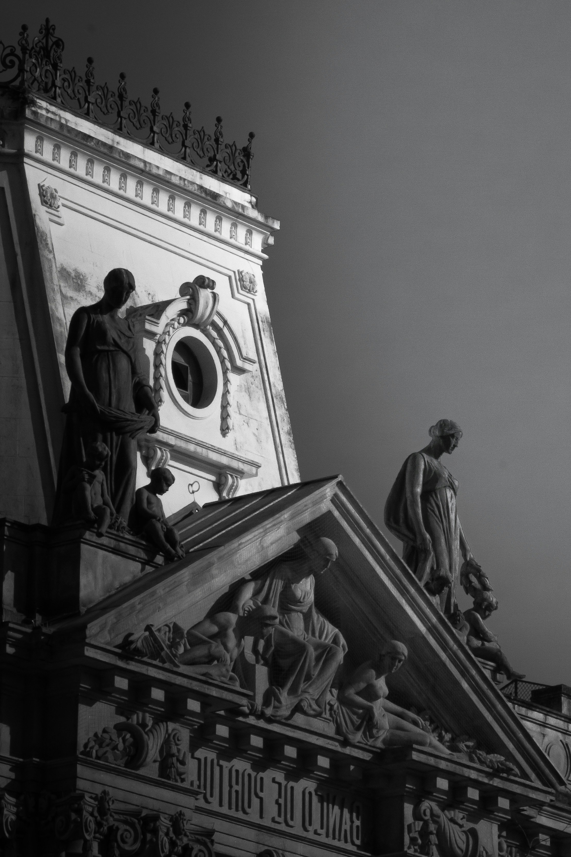 Statues adorn a historic building's facade, highlighted by contrasting light and shadow under a gray sky.