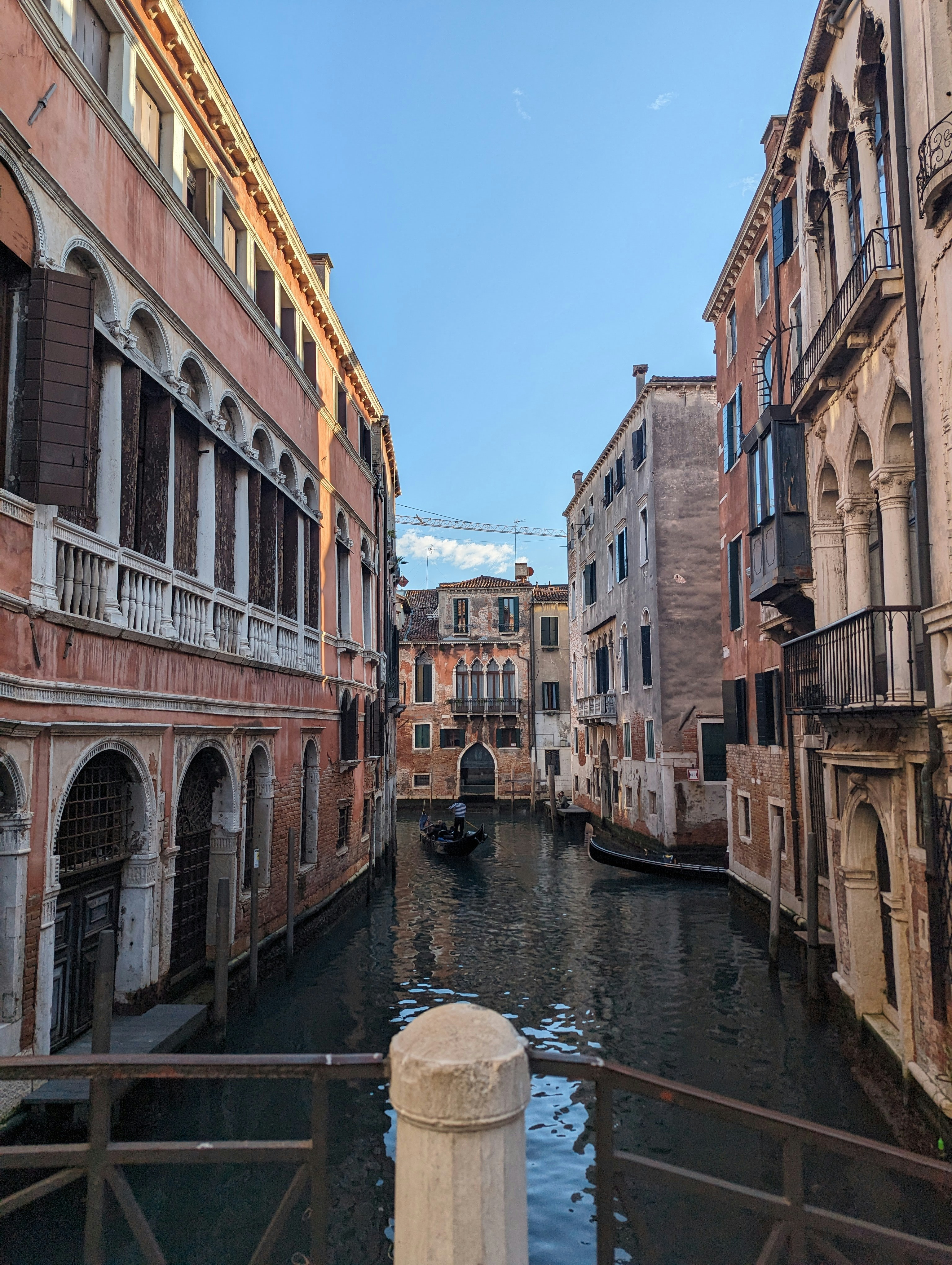 Quiet canal flanked by historic Venetian buildings under a clear blue sky.