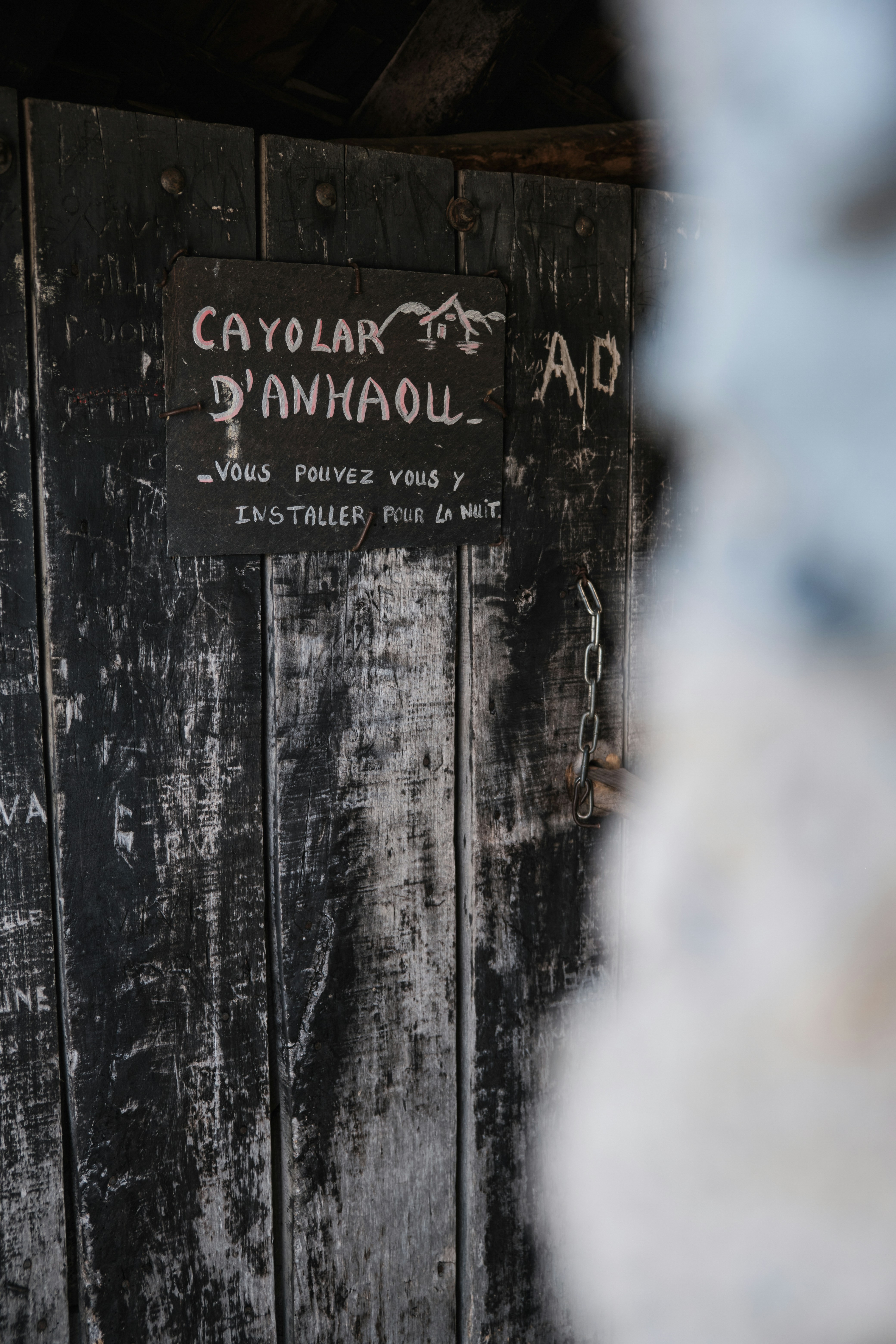 Weathered wooden wall with a whimsical sign featuring hand-painted text and illustrations.