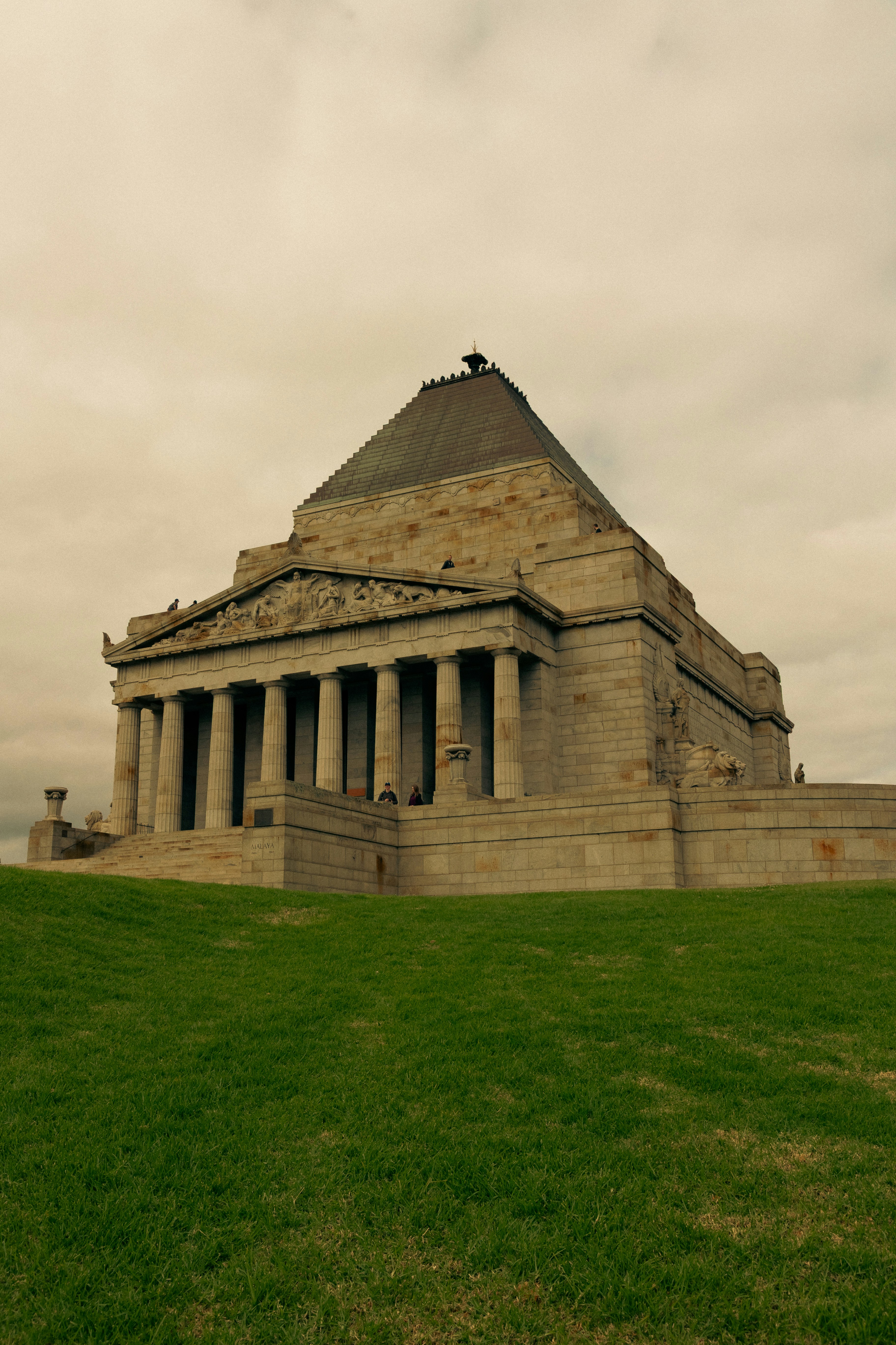 Grand stone mausoleum with a stepped roof and columns under a cloudy sky.