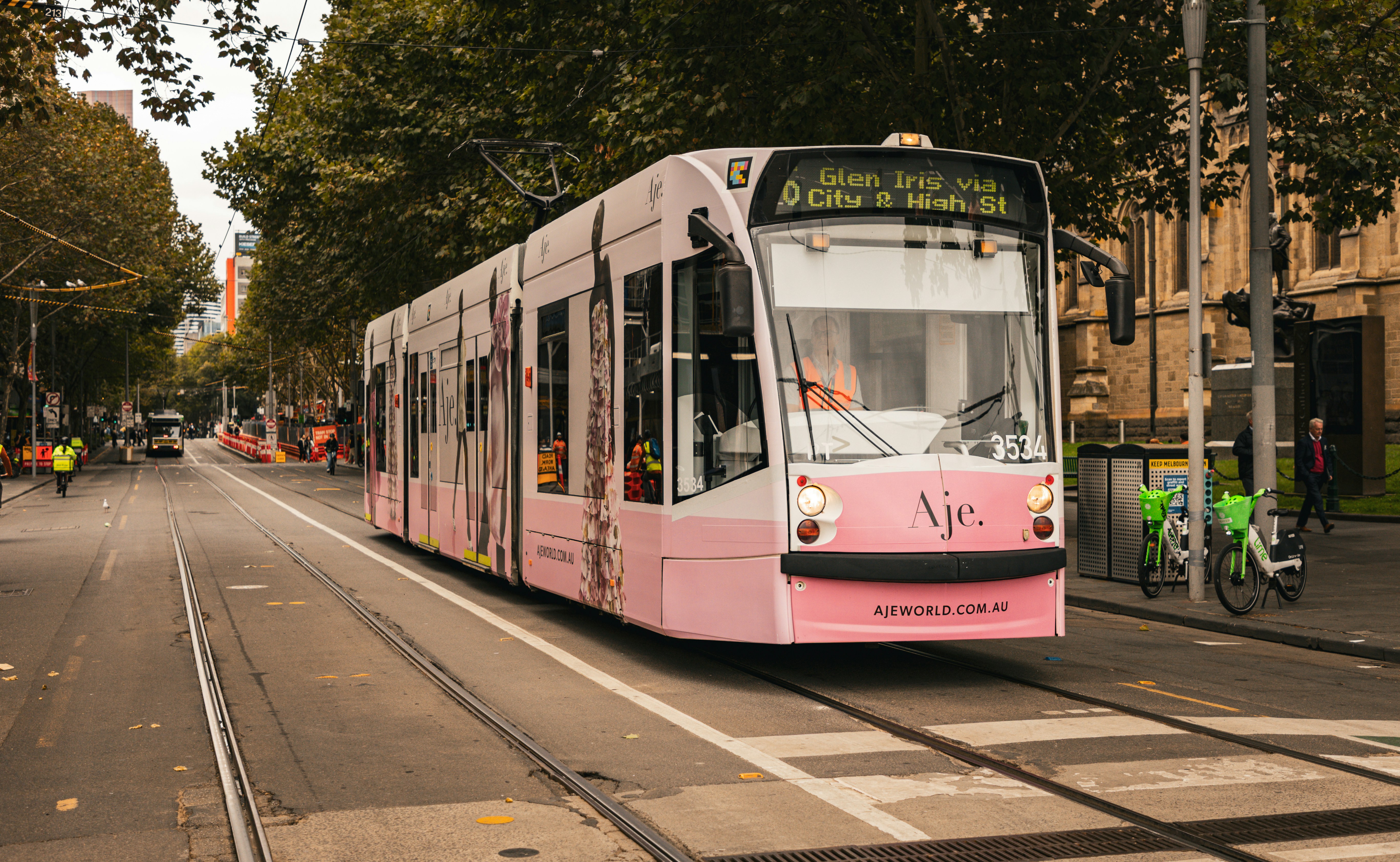 Petal-Pink Streetcar Gliding Through a Tree-Lined City Street
