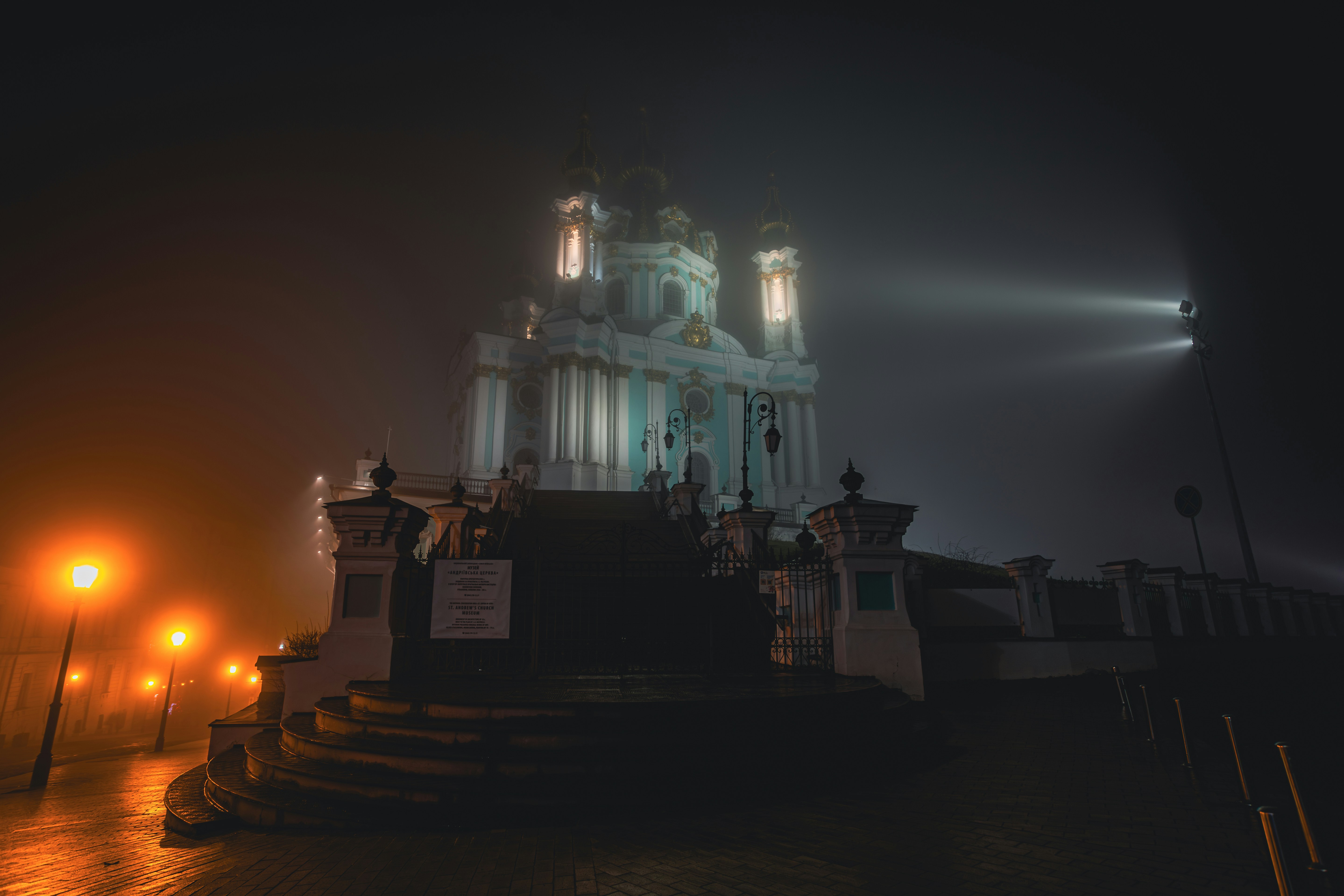 Illuminated cathedral shrouded in fog with glowing streetlights.