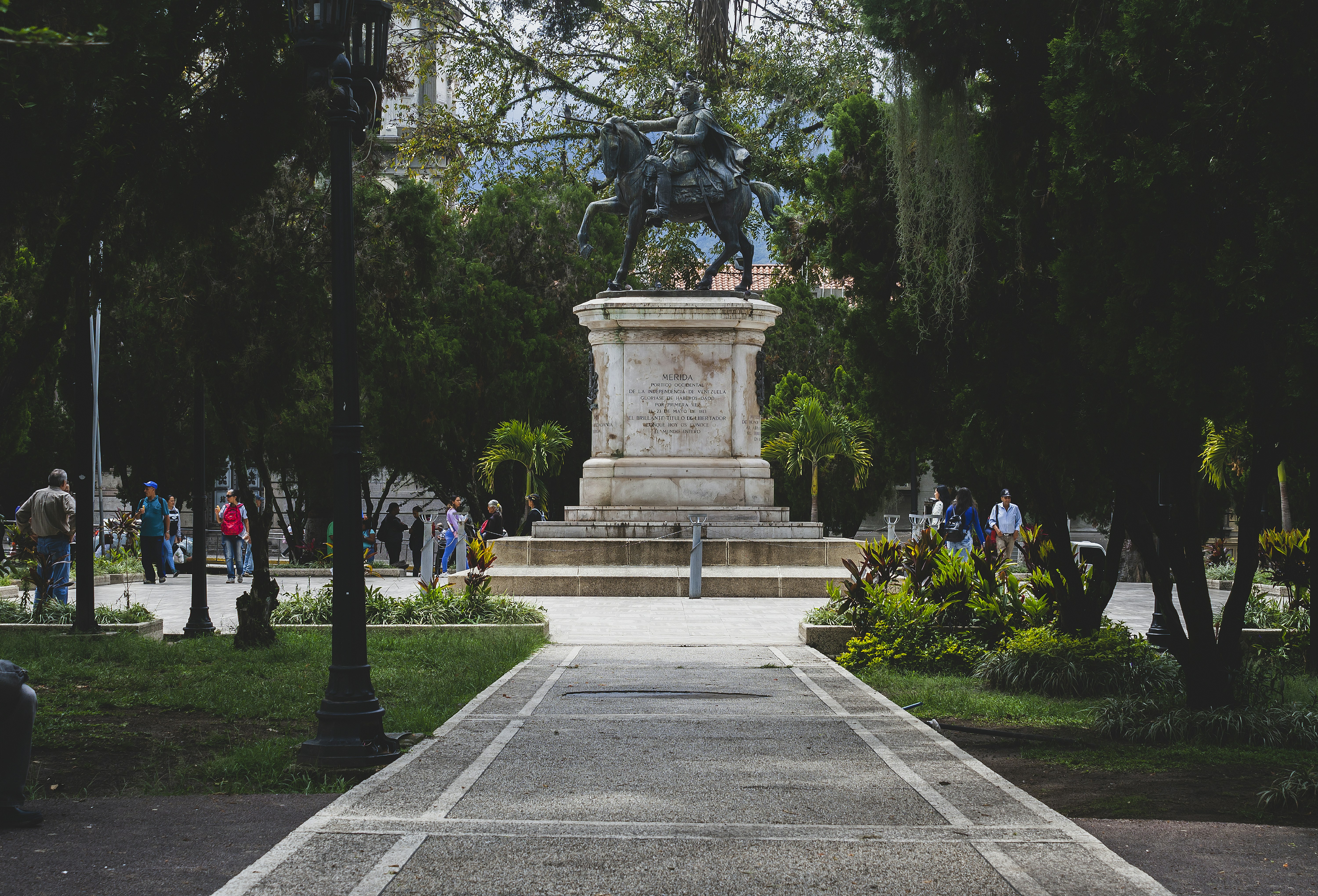 Bronze statue of a mounted figure stands prominently in a park, surrounded by lush greenery and visitors enjoying the serene atmosphere.