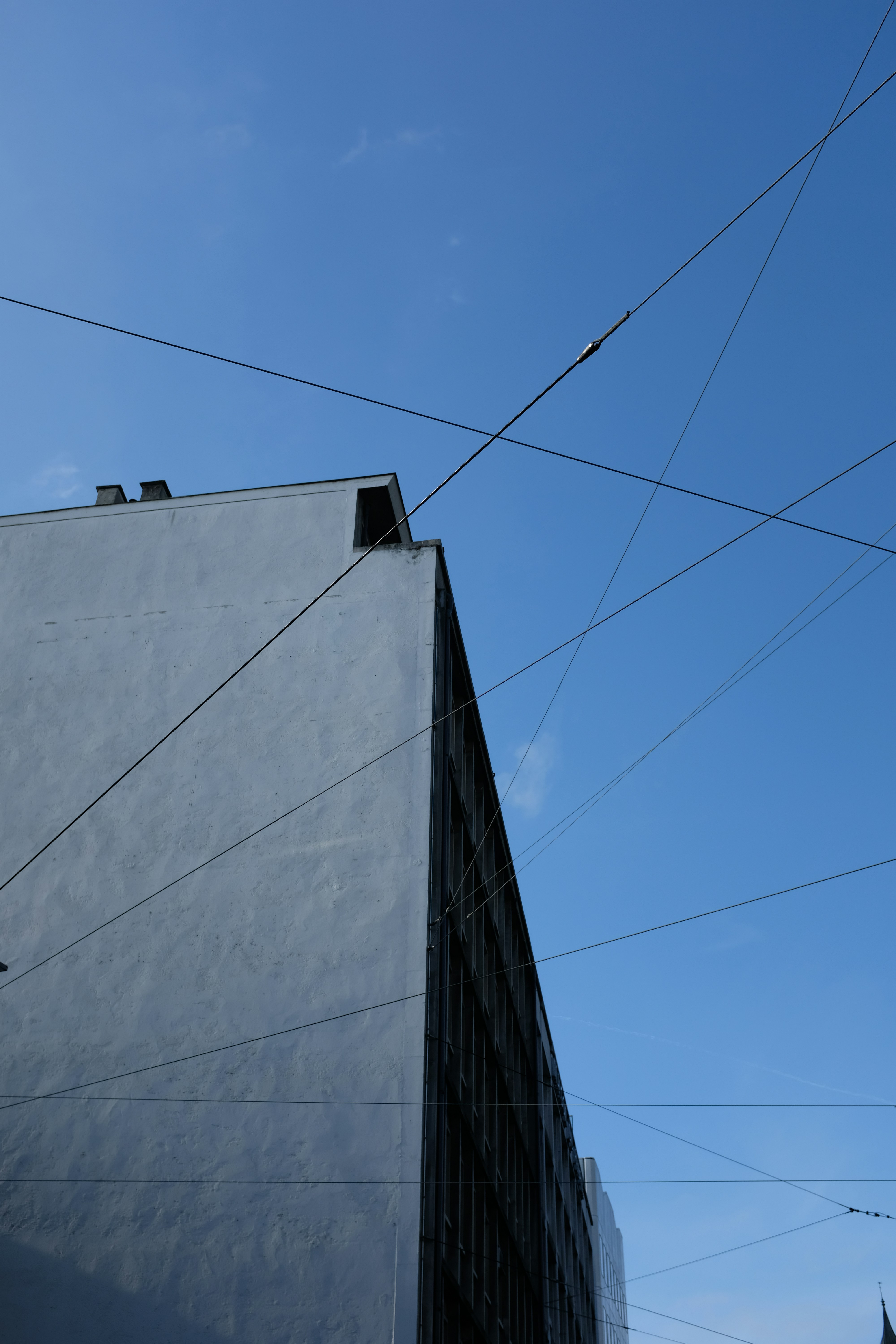 Building facade intersected by overhead cables under a clear blue sky.