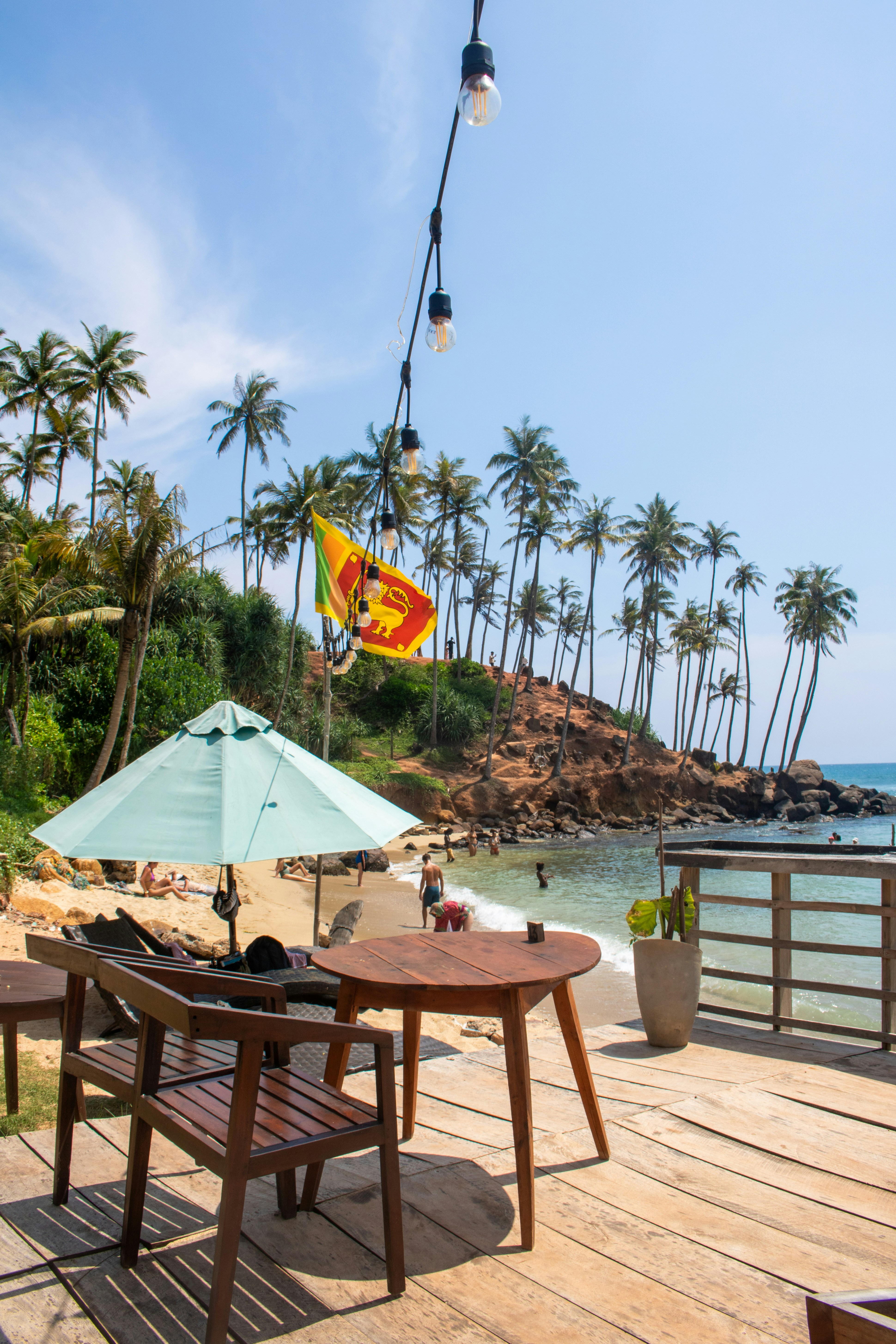 Wooden deck overlooking a sandy beach with tall palm trees under a clear blue sky.