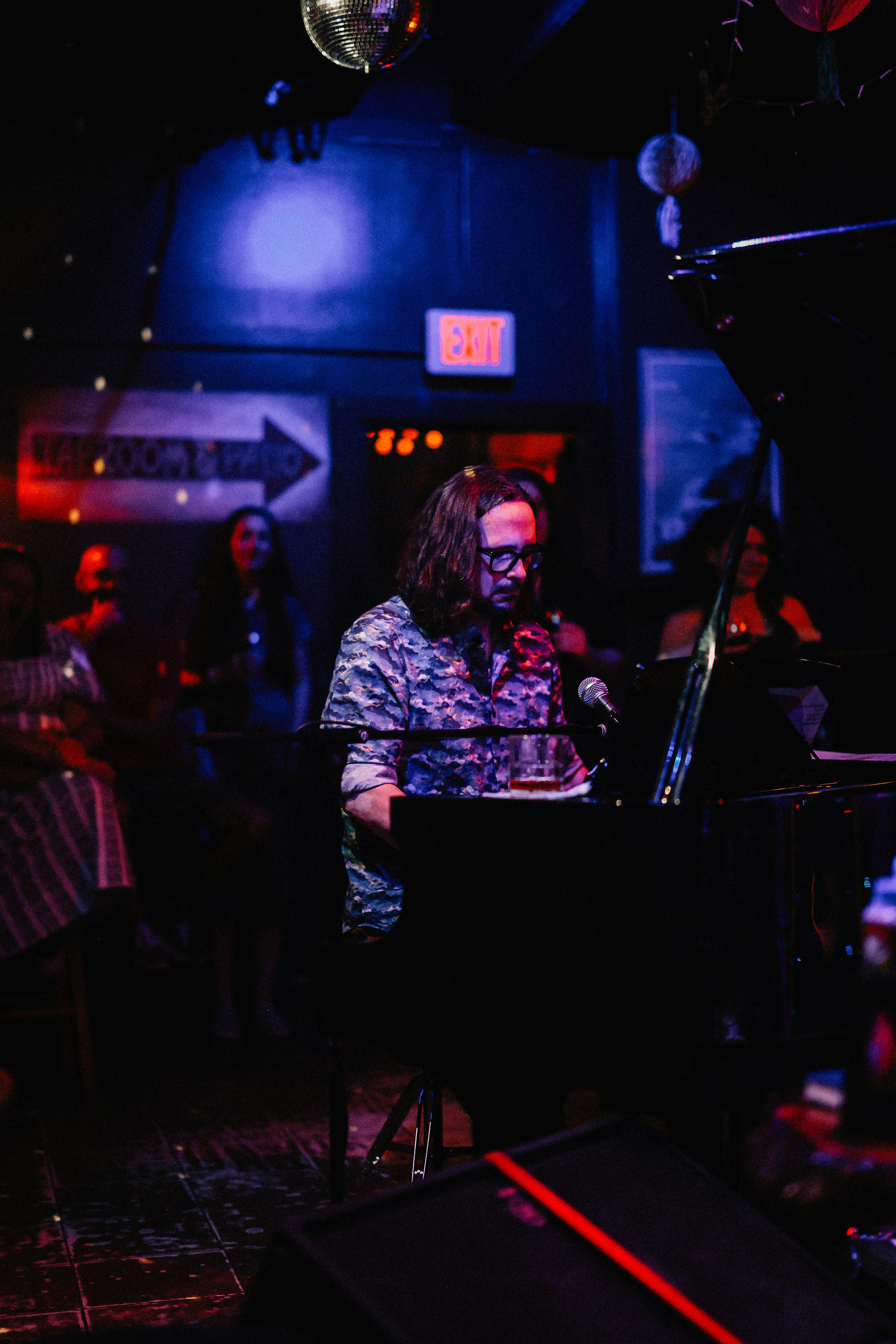 Musician passionately playing the piano in a dimly lit venue, surrounded by an engaged audience. A vibrant atmosphere enhances the intimate performance.
