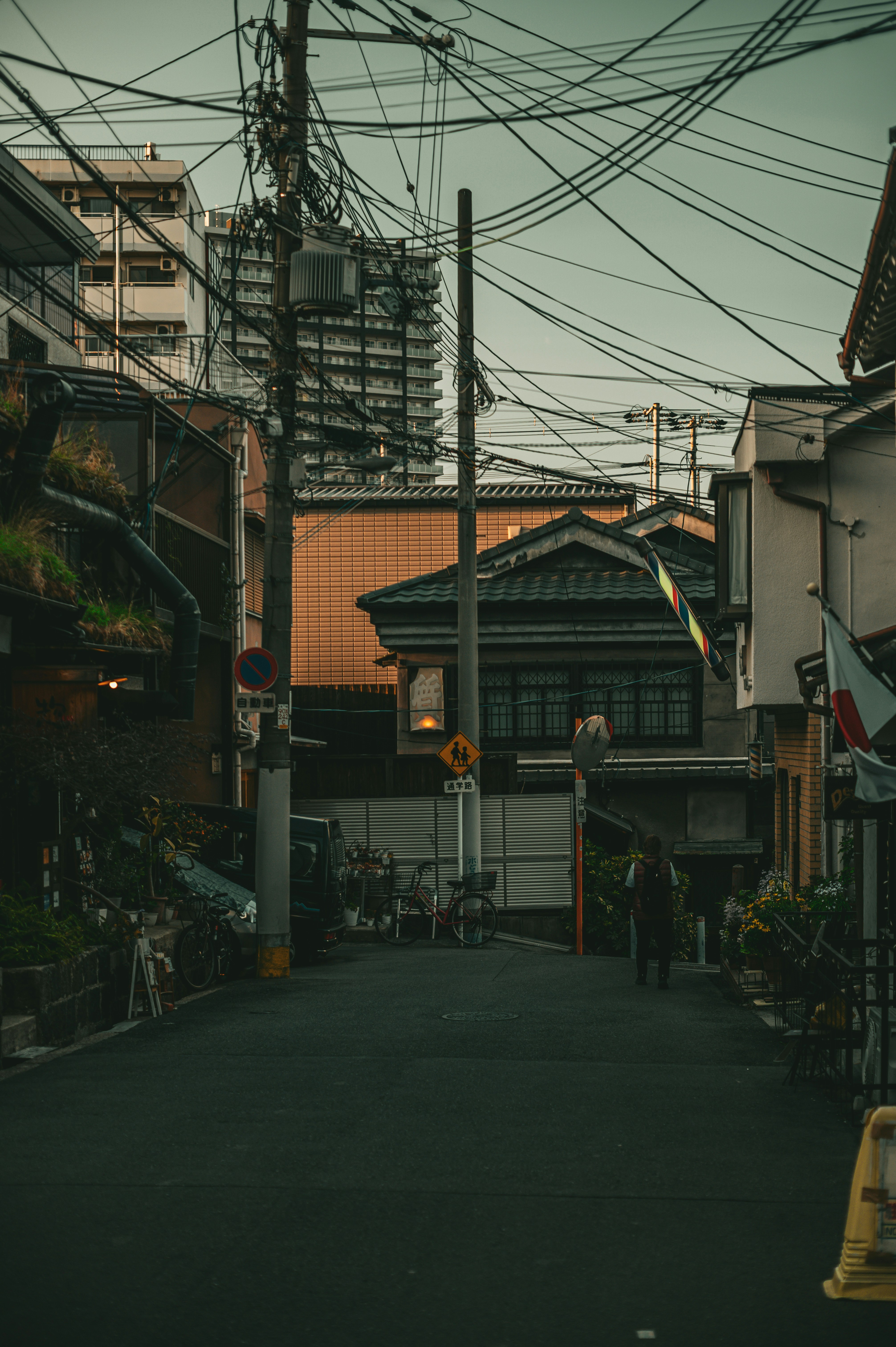 Quiet street scene with tangled wires overhead and buildings lining the path at dusk.