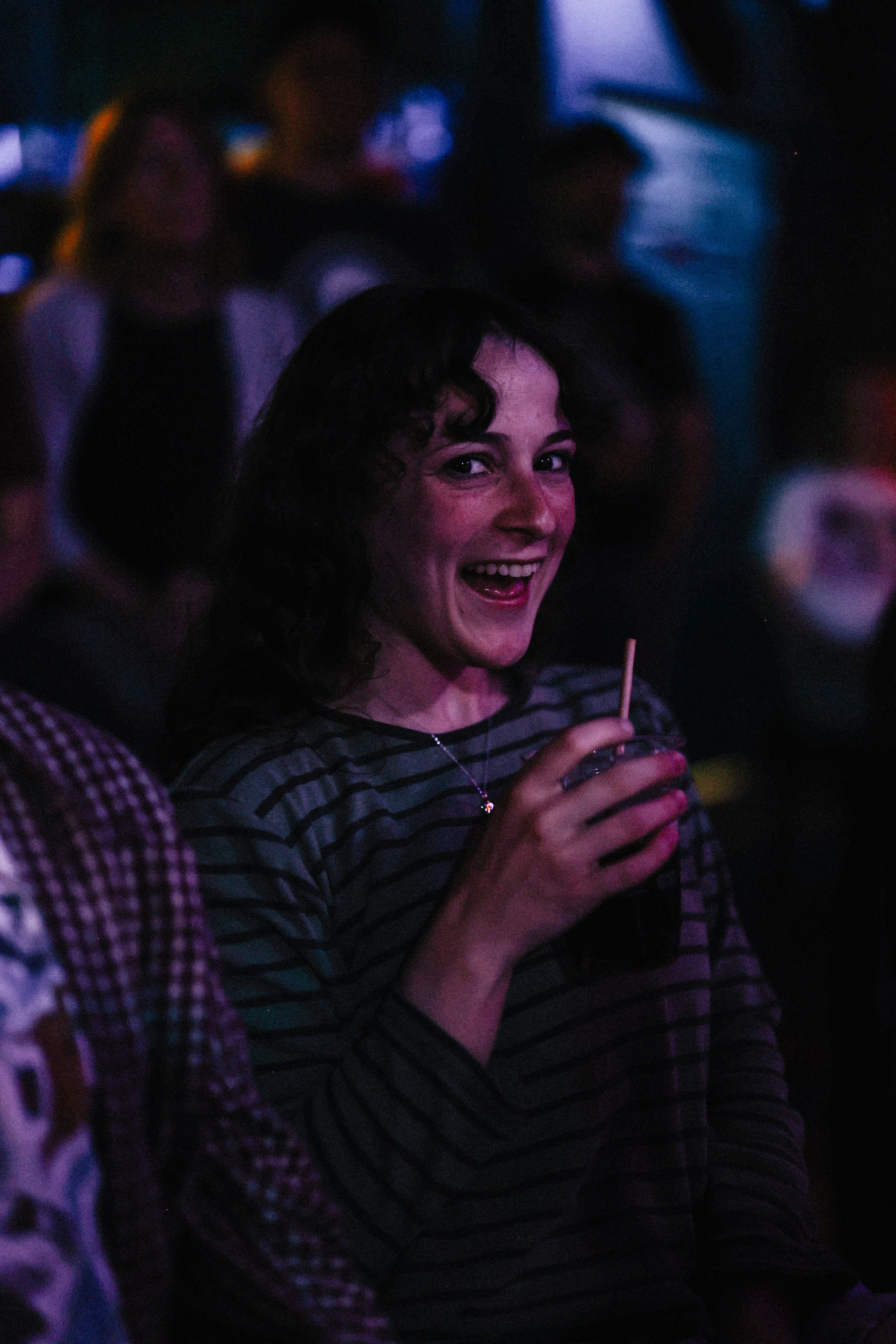 Smiling woman holds a drink in a dimly lit place. photo – Free Woman ...