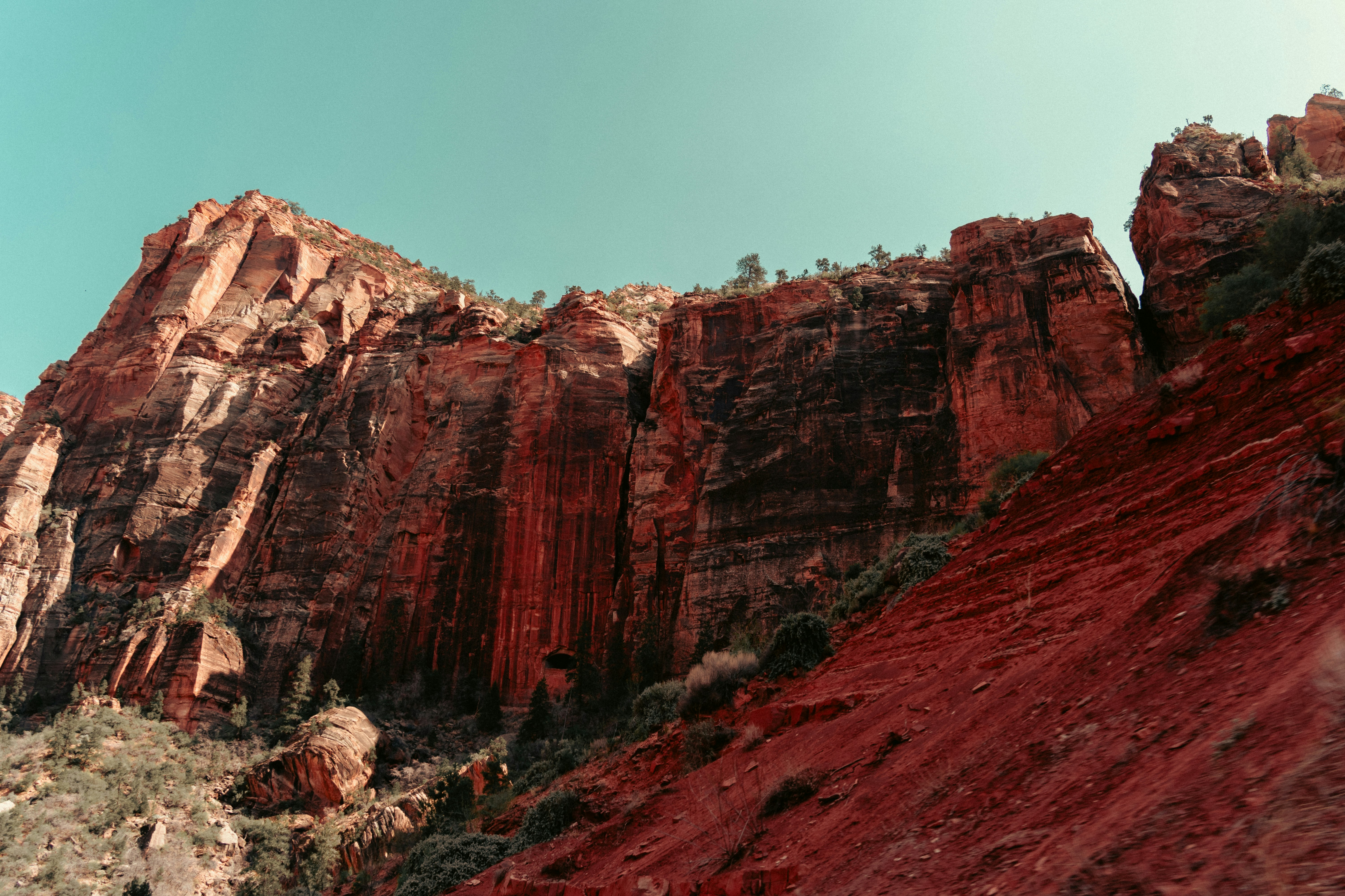 Massive red rock formations rise against a clear blue sky in a rugged landscape.