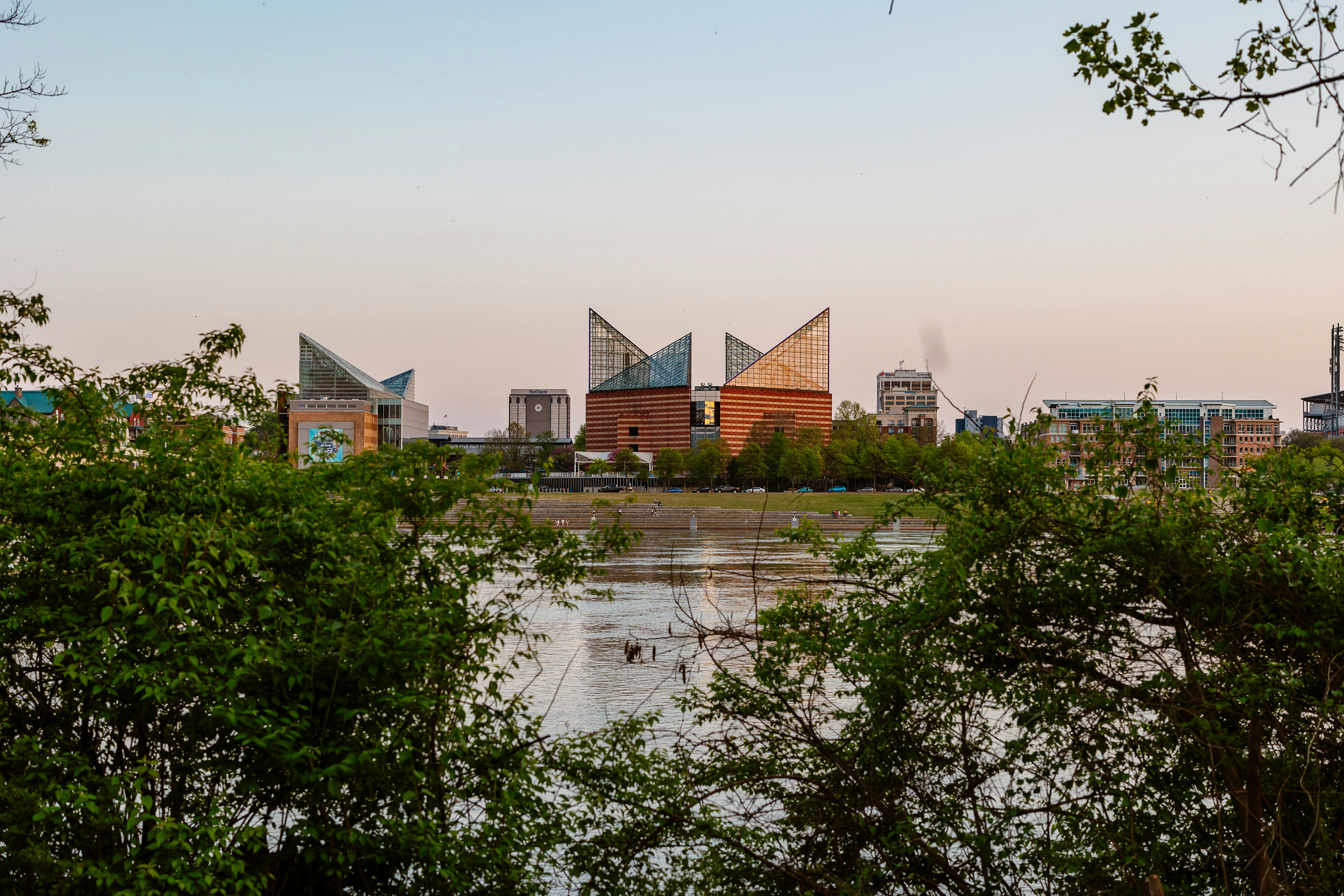Chattanooga aquarium skyline framed by lush greenery and a calm river at sunset.