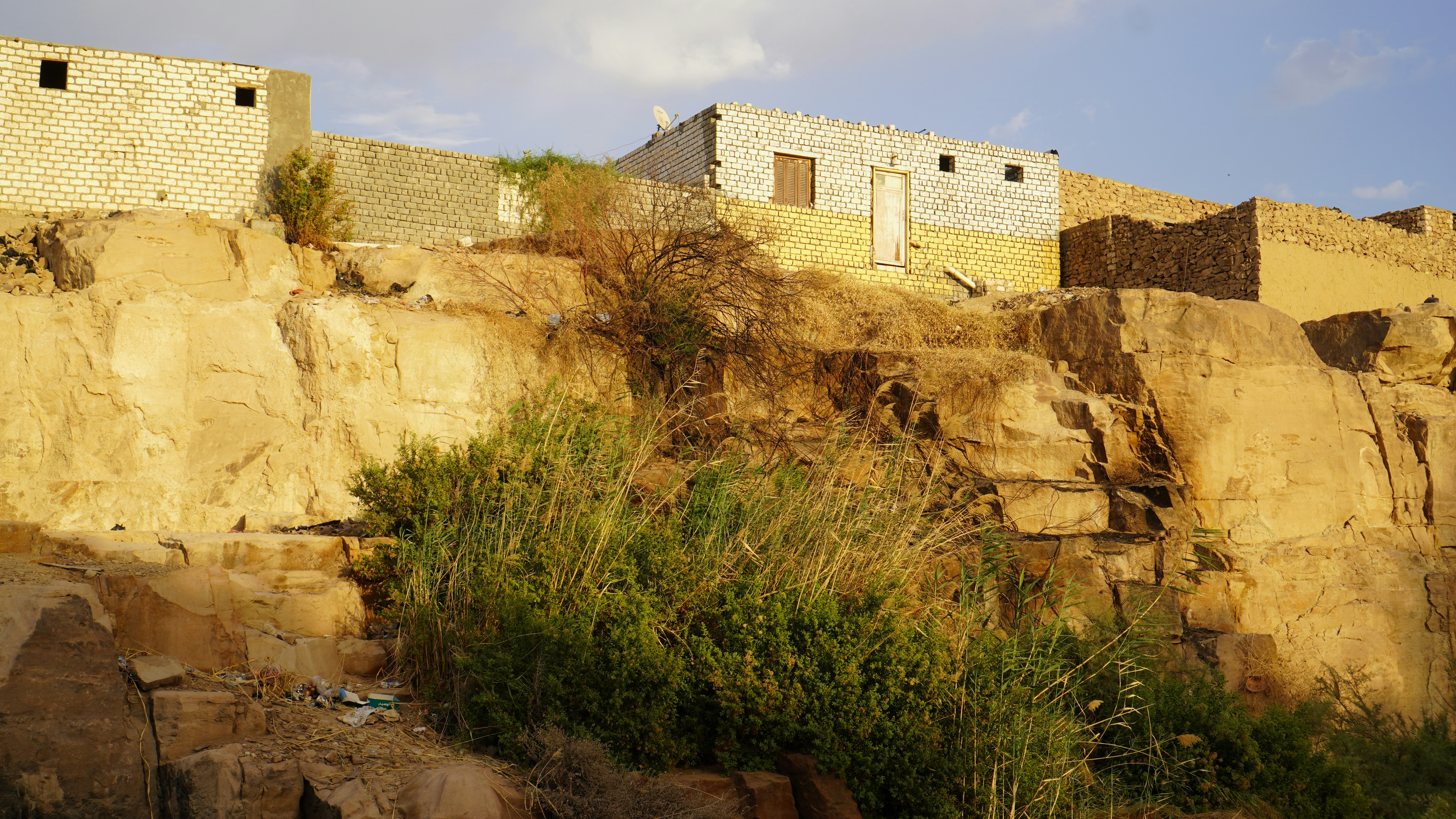 A rugged cliffside adorned with simple structures, showcasing the intersection of human habitation and natural landscape. Greenery thrives amidst the rocky terrain.