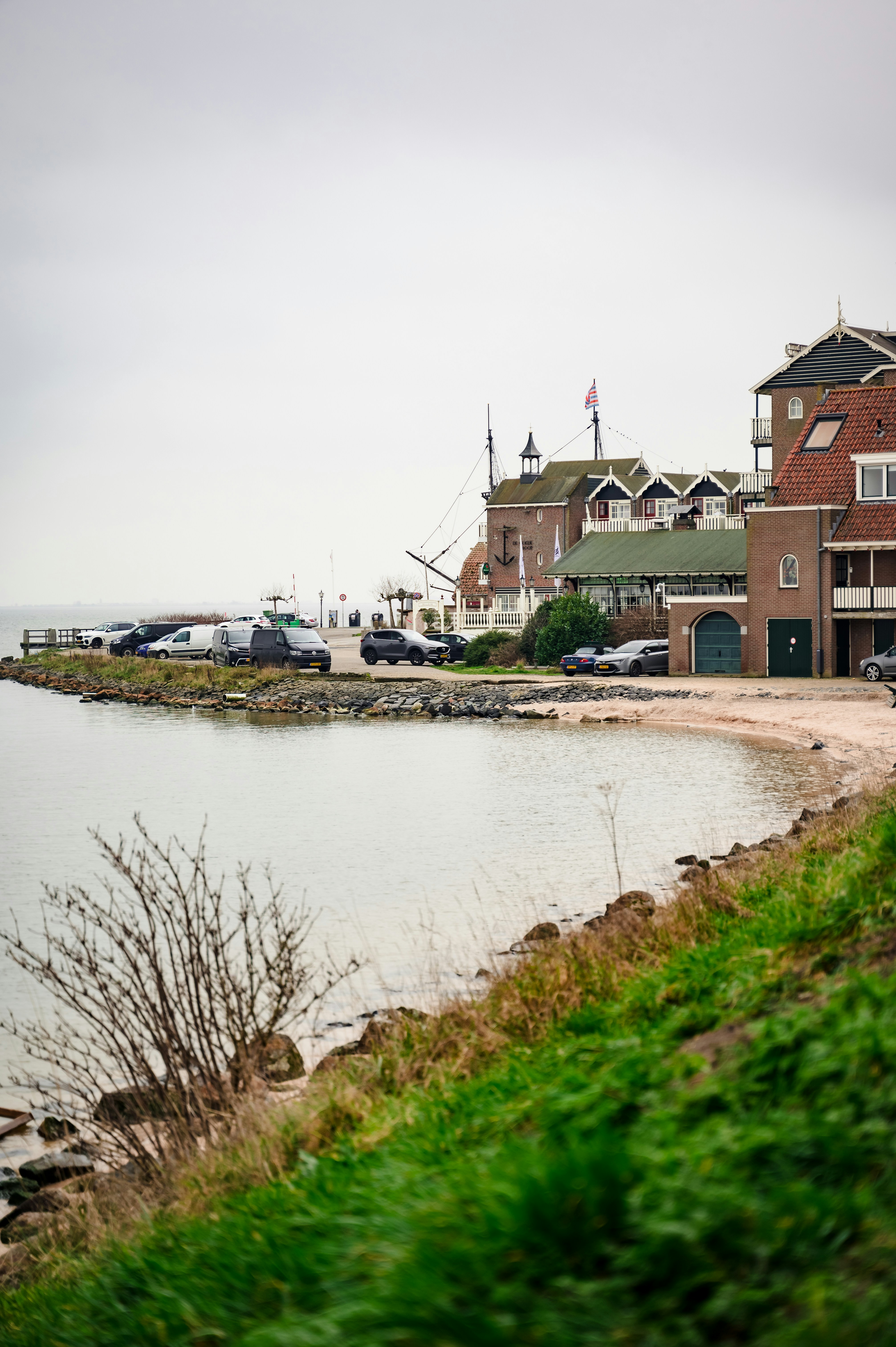 Quaint harbor with brick buildings and gentle waves under an overcast sky.