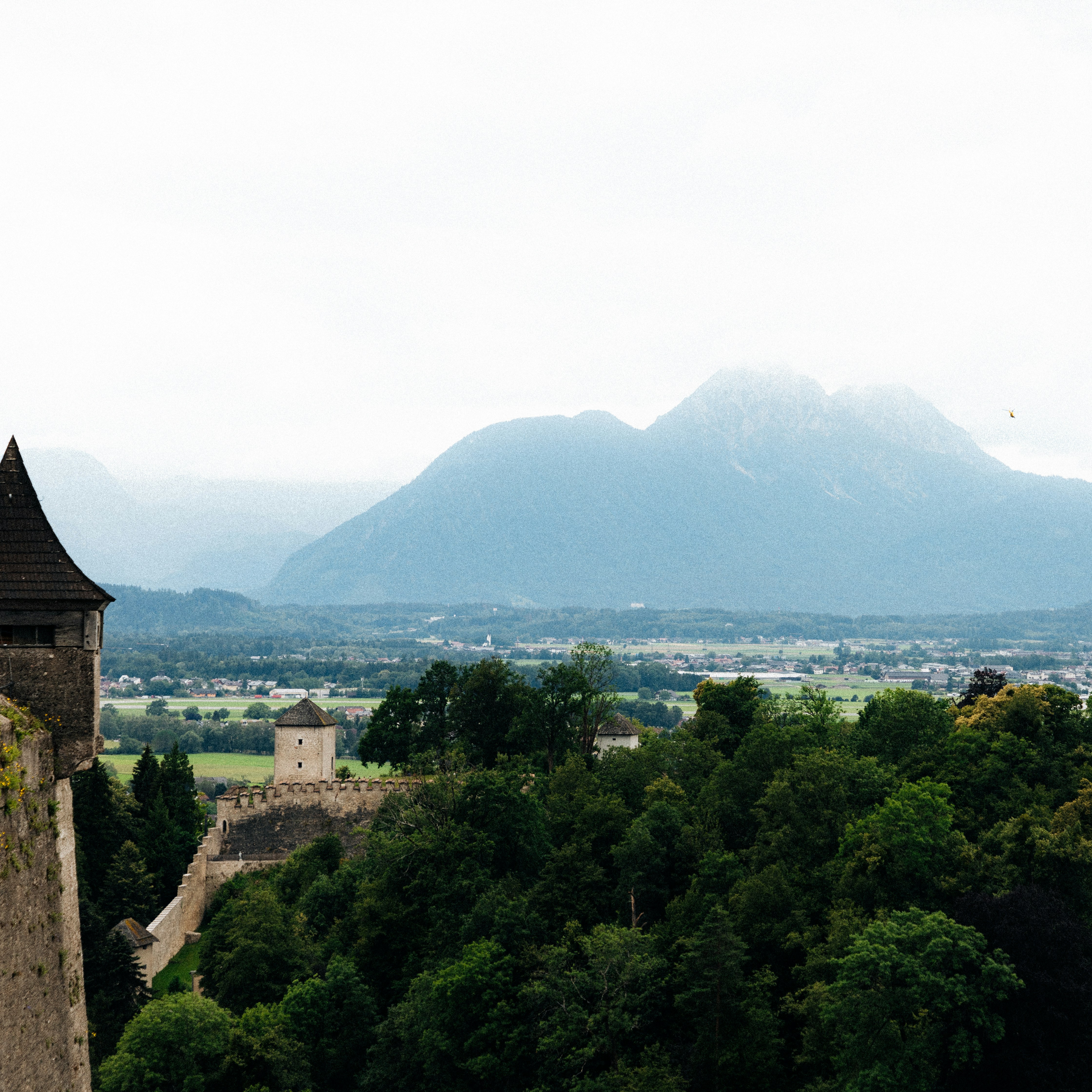 Historic castle wall overlooking lush green forest and distant misty mountains.