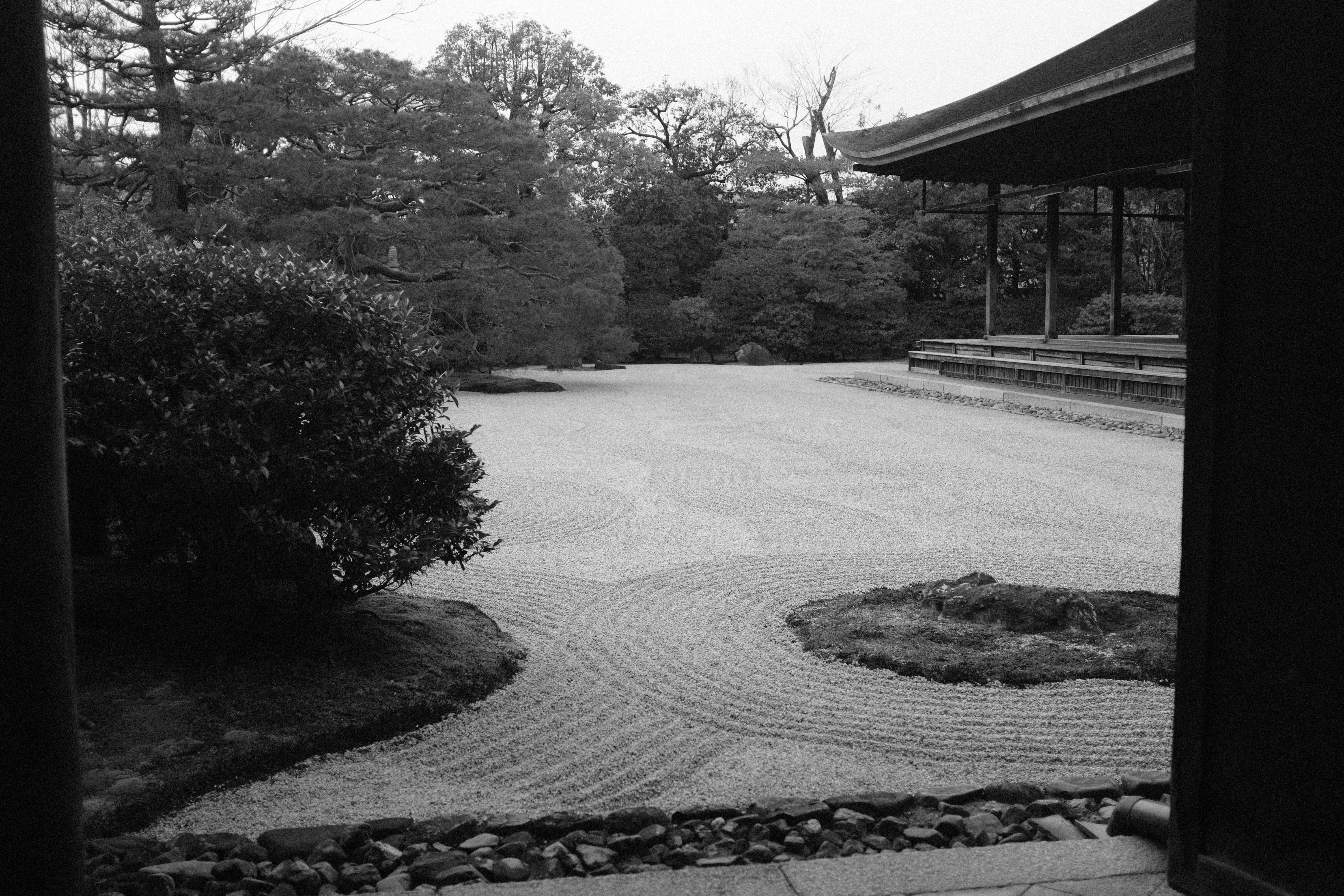 Black and white view of a Zen garden with raked gravel patterns and traditional wooden architecture.