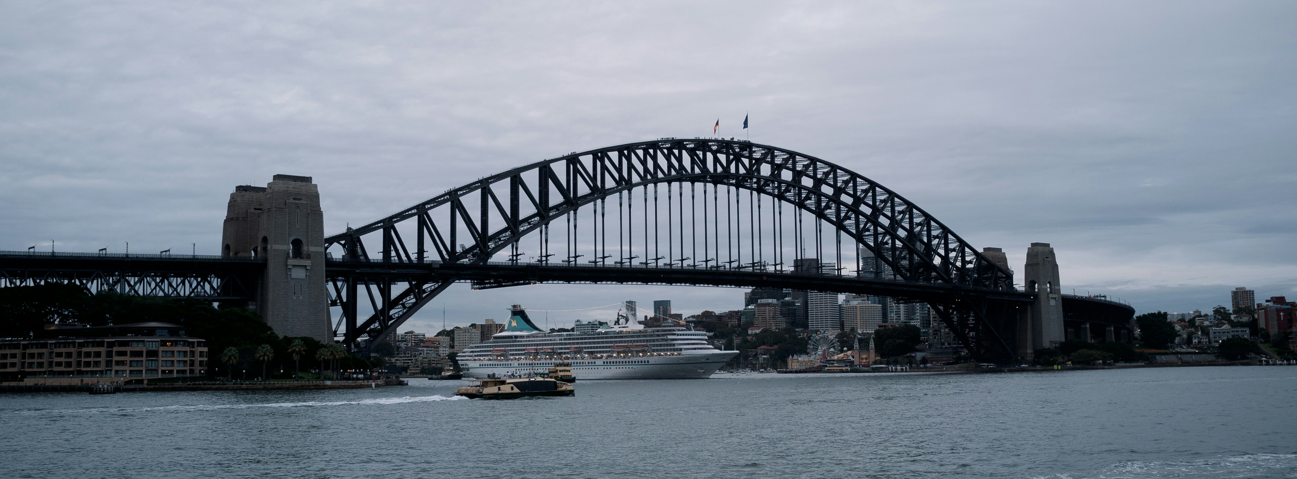Iconic steel arch bridge spanning a harbor under a cloudy sky.